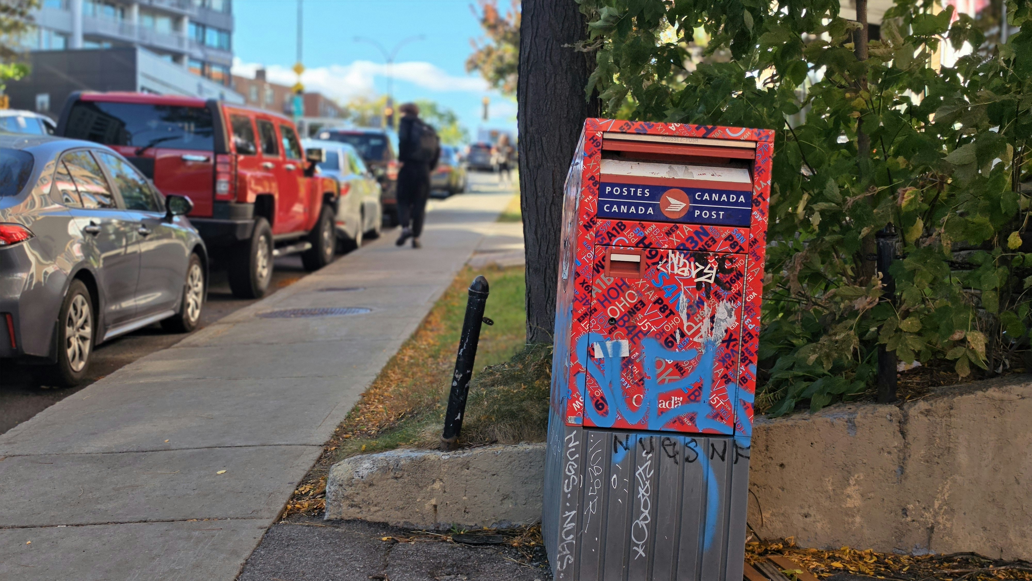 Graffiti-blanketed mailbox on a sunlit urban curb