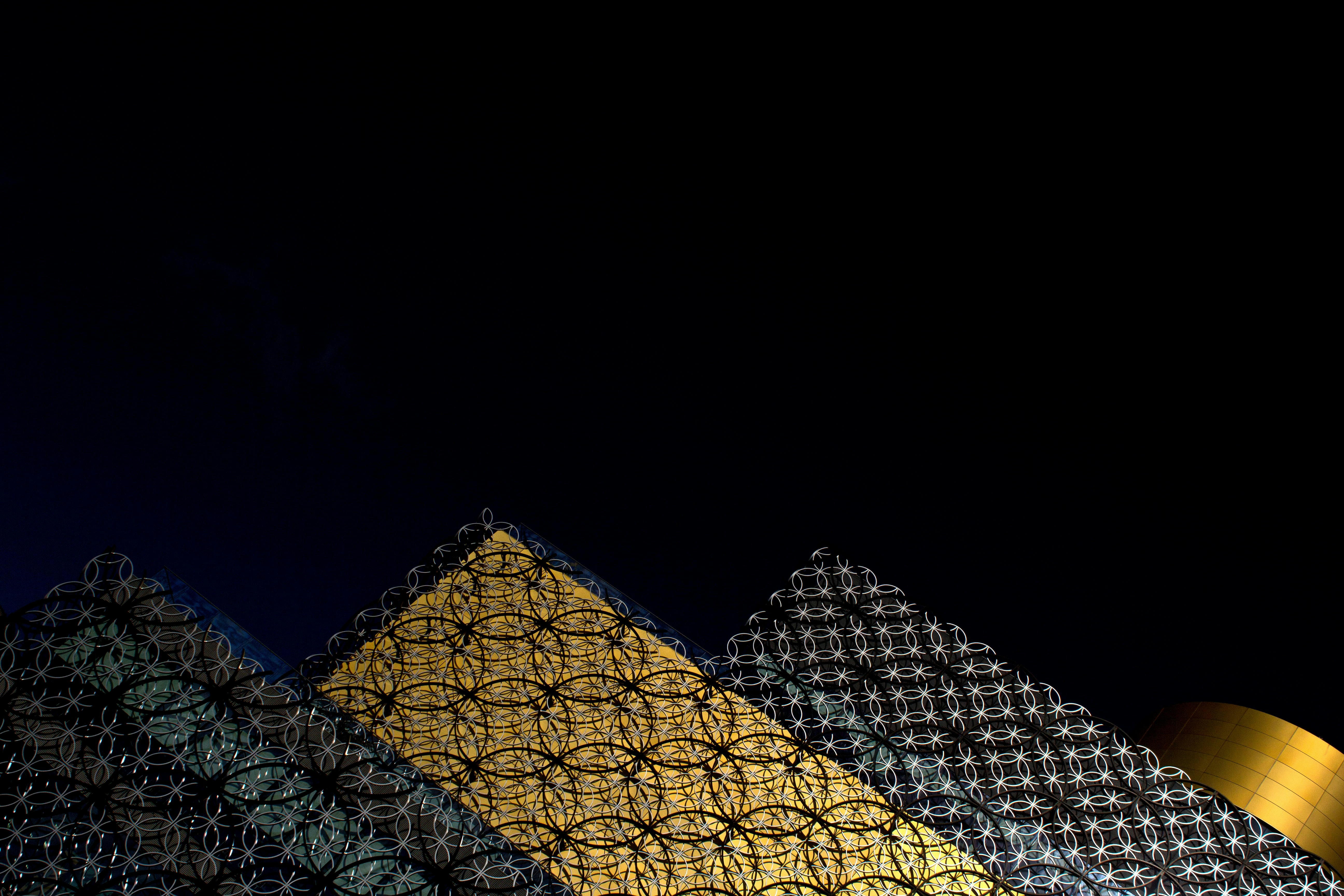 Close-up of three ornate, diamond-patterned metal tiles (green, gold, silver) set against a dark night sky, with subtle gloss and a hint of a gold rim on the right. This is a decorative installation display.