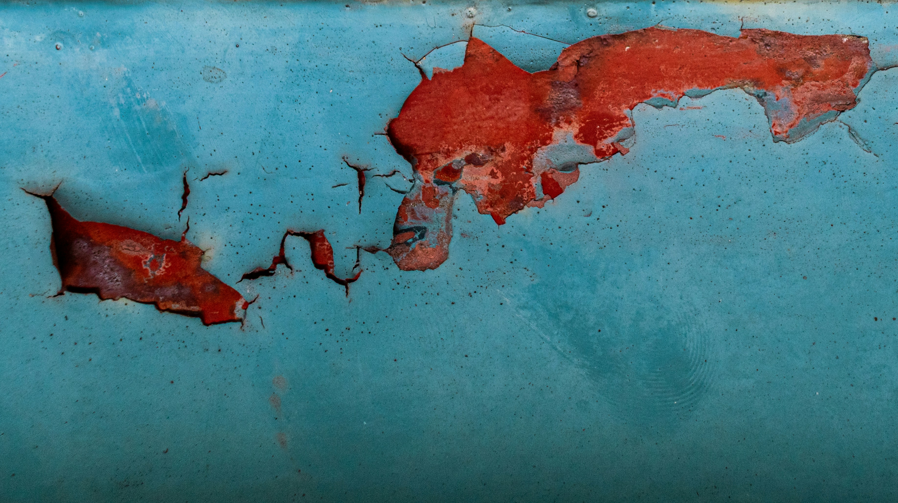 Peeling turquoise paint exposing red patina in a weathered surface