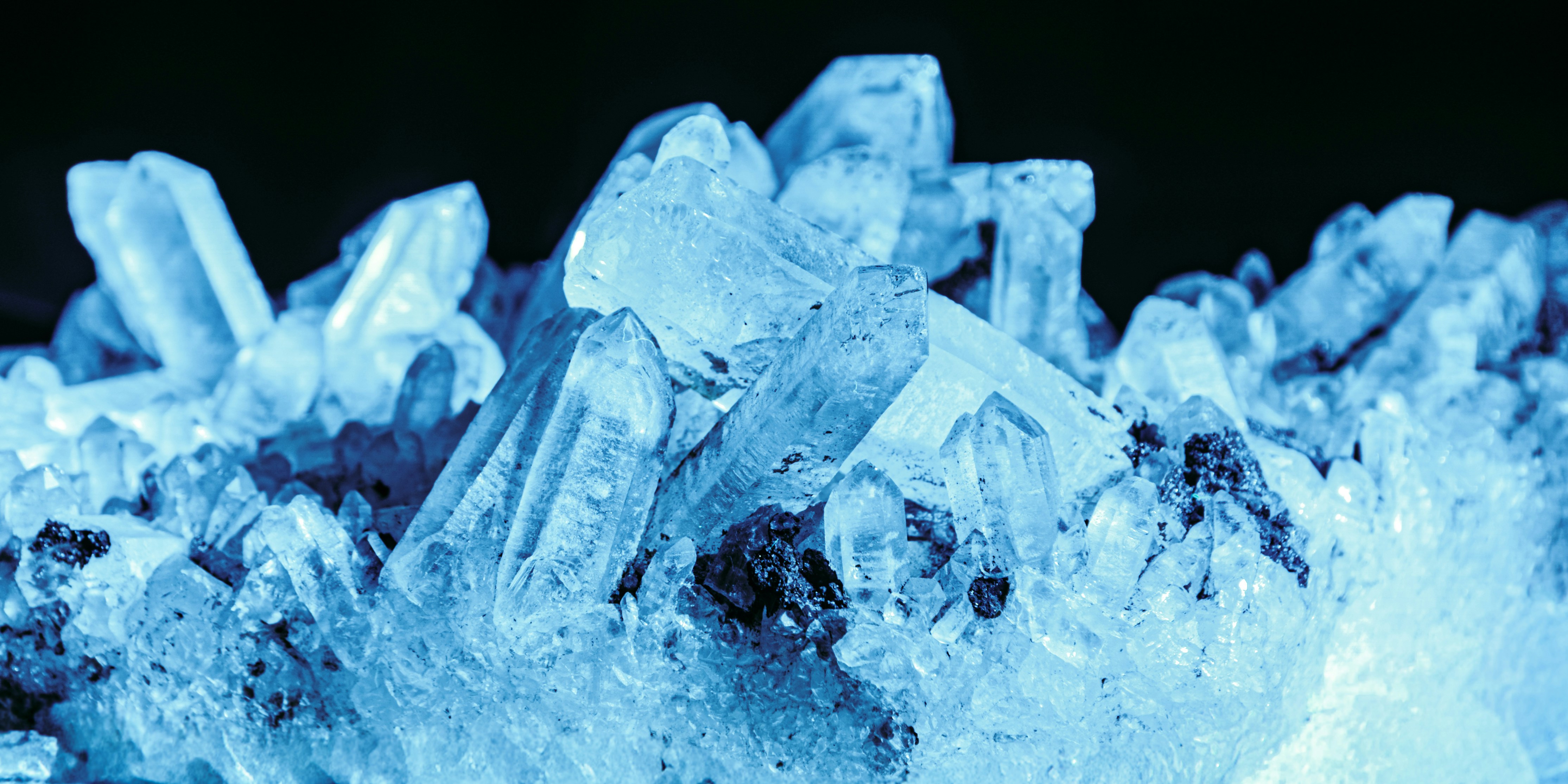 Close-up of vibrant blue crystal clusters with sharp facets and icy texture, set against a dark backdrop to emphasize color and structure.