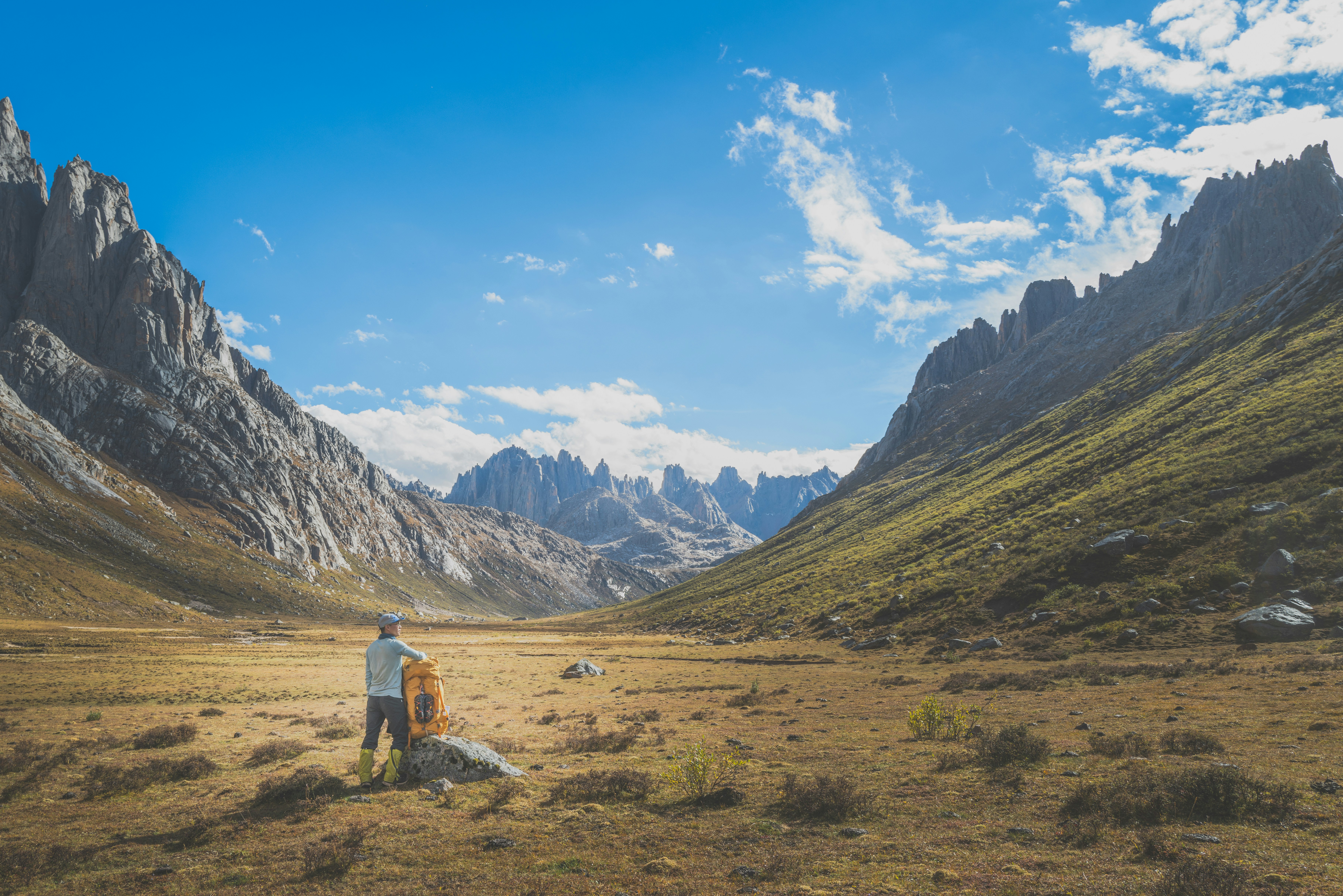 Two hikers in a sunlit alpine valley with jagged peaks