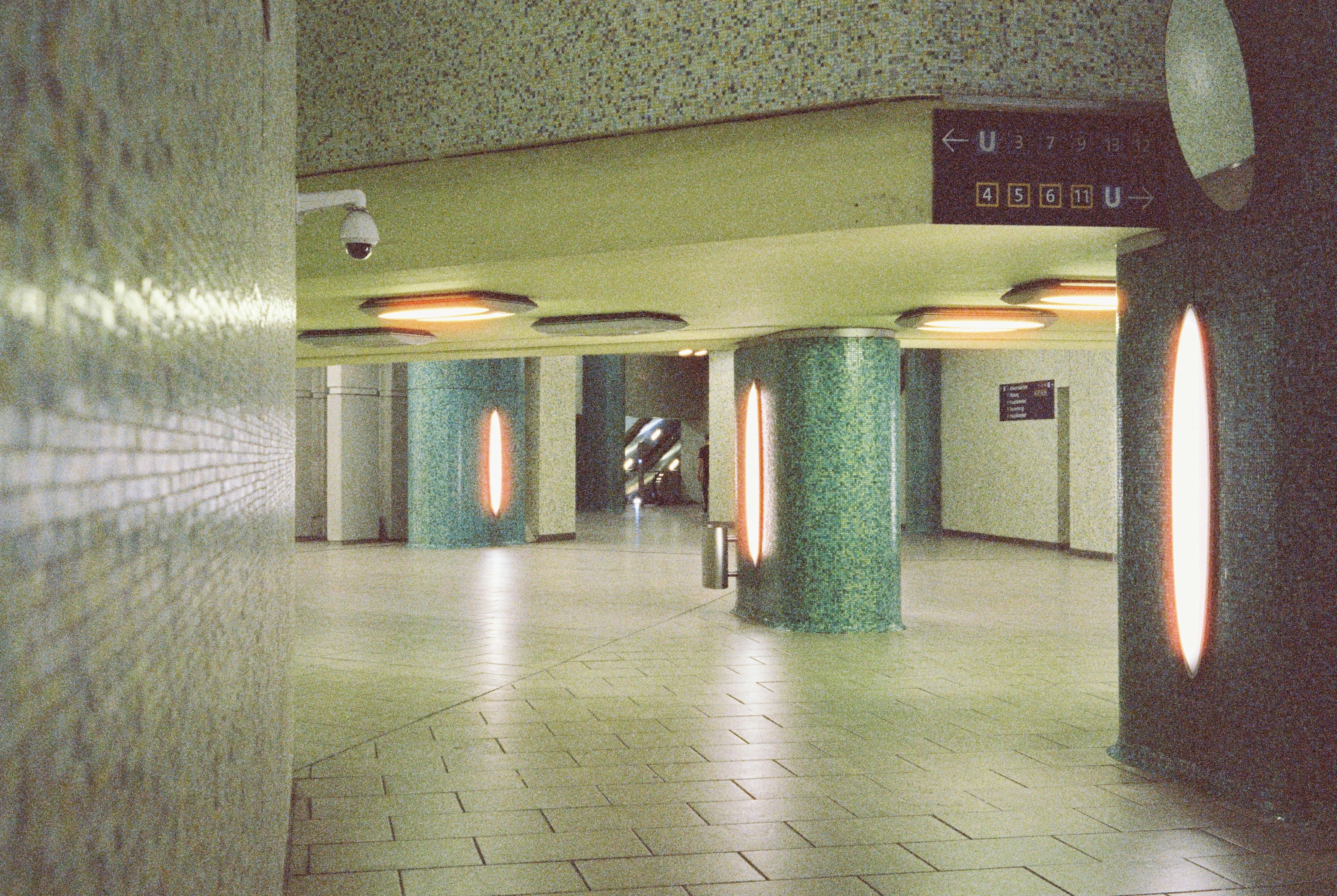 Underground corridor with curved green pillars and warm neon lights along the walls, creating a moody, retro atmosphere.