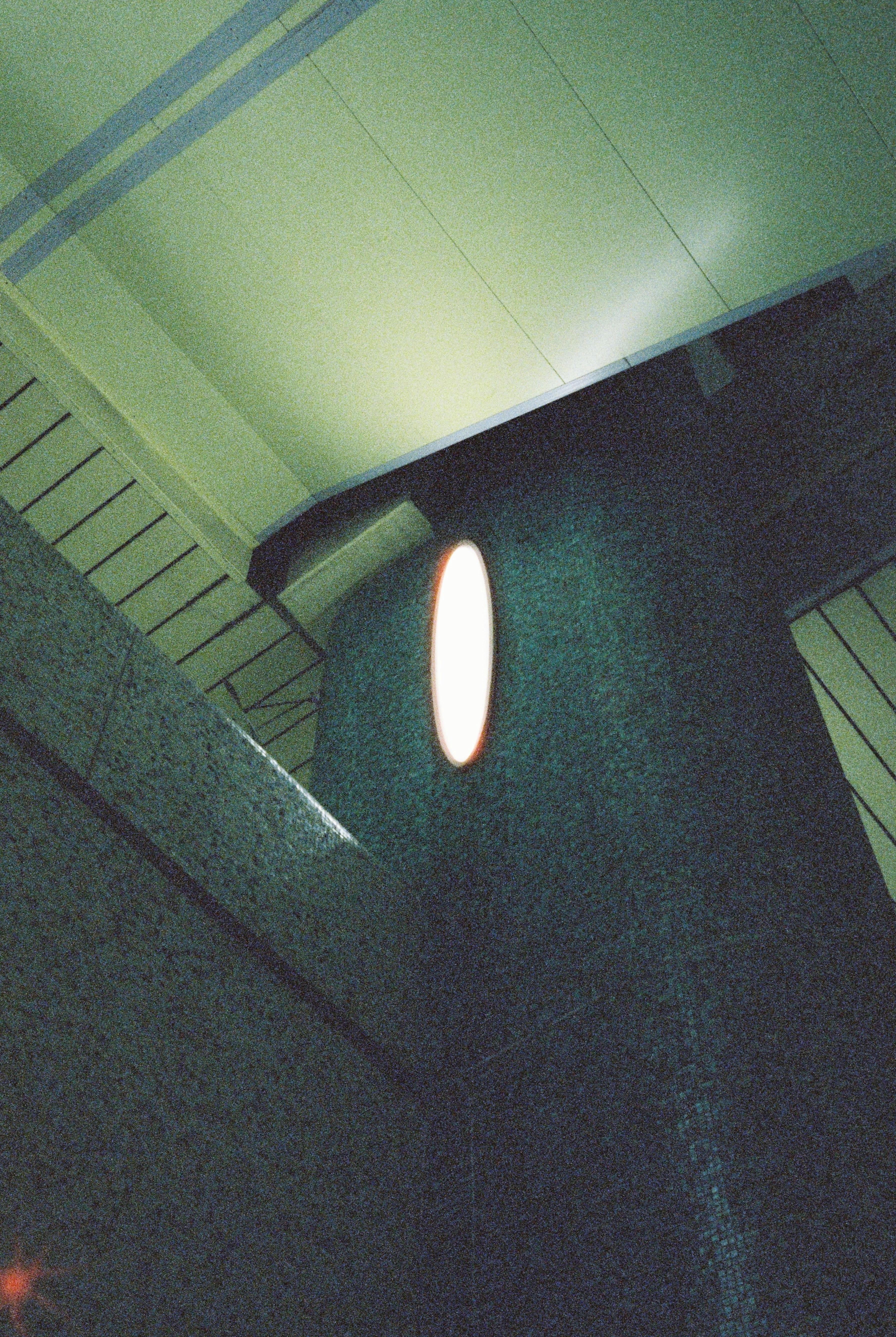 Dim, moody sculpture-like interior with a single illuminated oval glow set against textured walls and geometric lines. The scene emphasizes ambient lighting and grainy texture over architectural detail.
