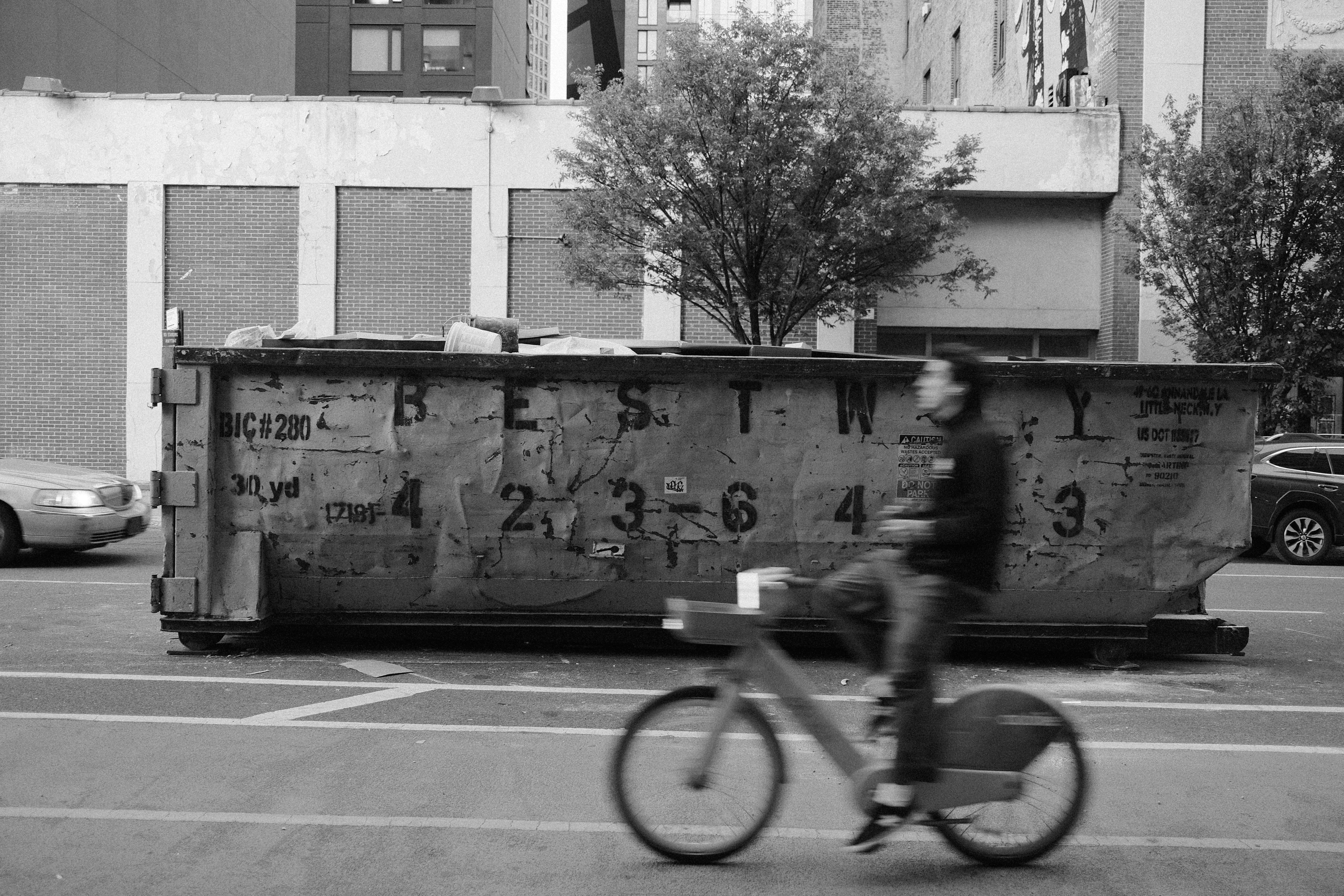 Motion through stillness: cyclist in front of a weathered city dumpster