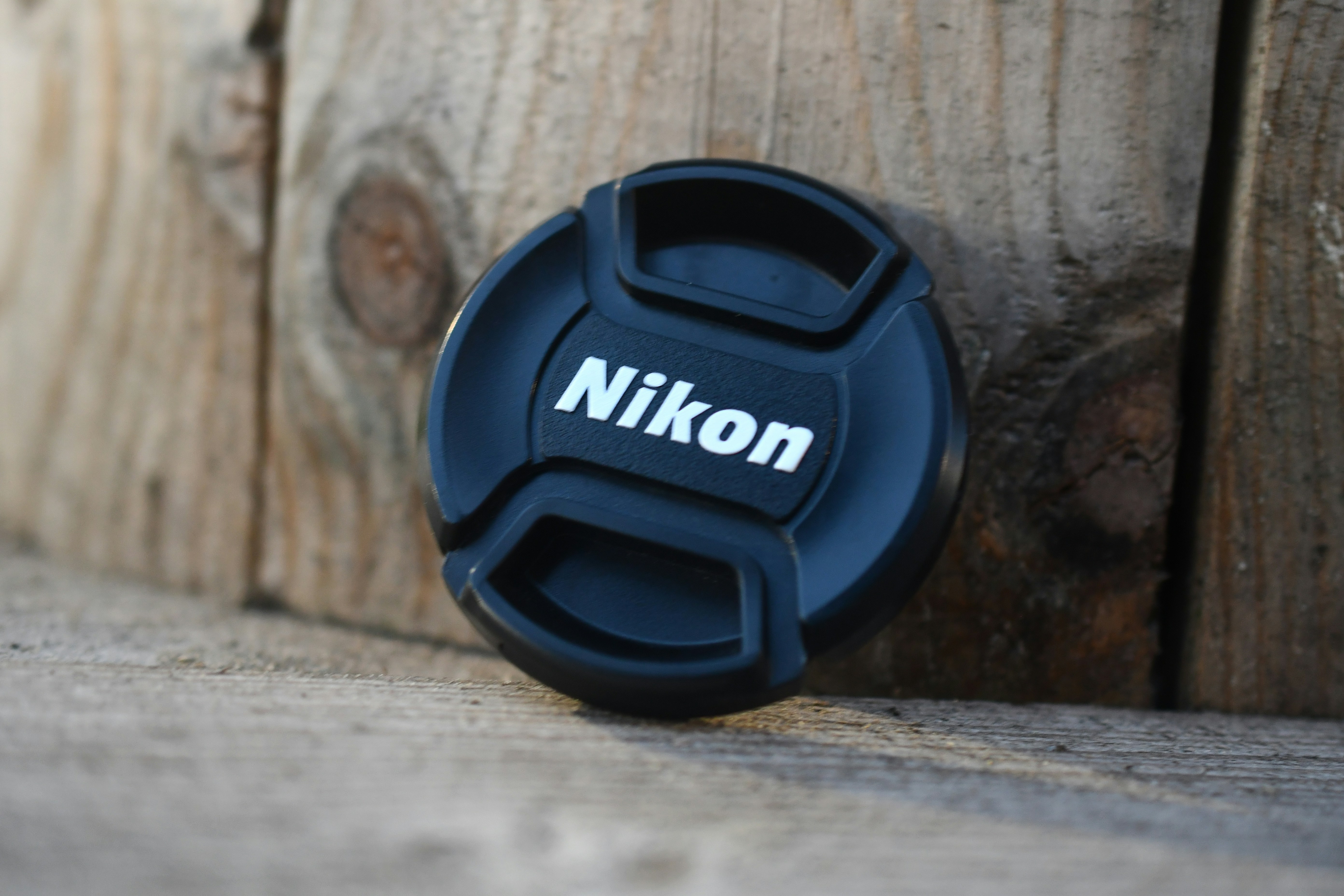 Nikon Centered: A Close-Up on a Lens Cap Resting Against Wood