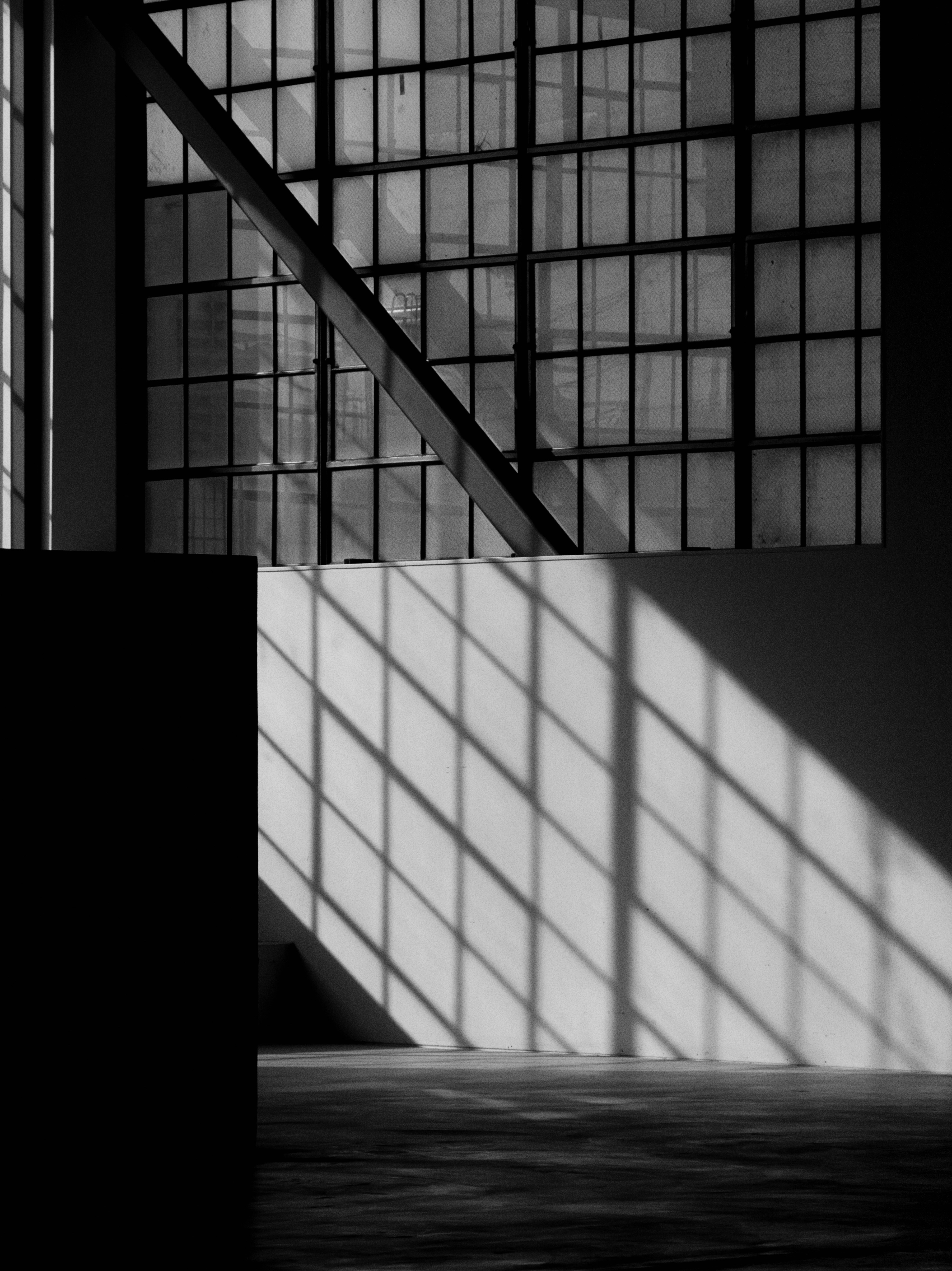 Grid shadows cast by a large industrial window onto a white wall in black and white