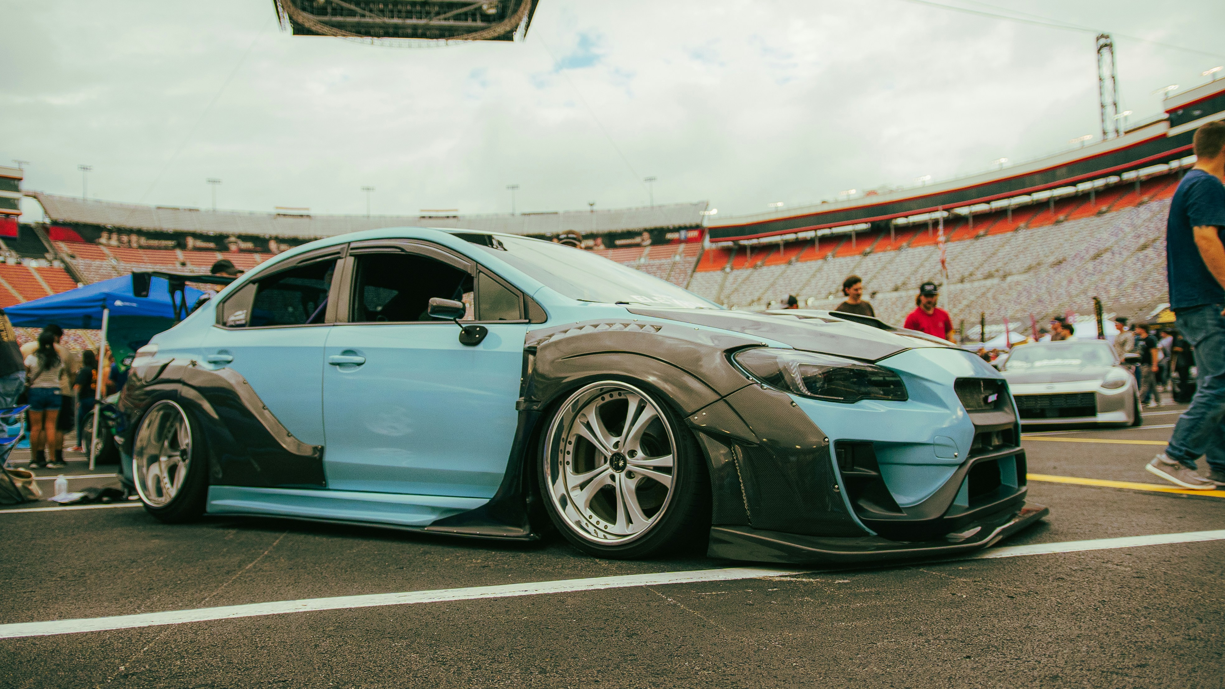 Low-slung blue race–styled coupe at a crowded automotive show