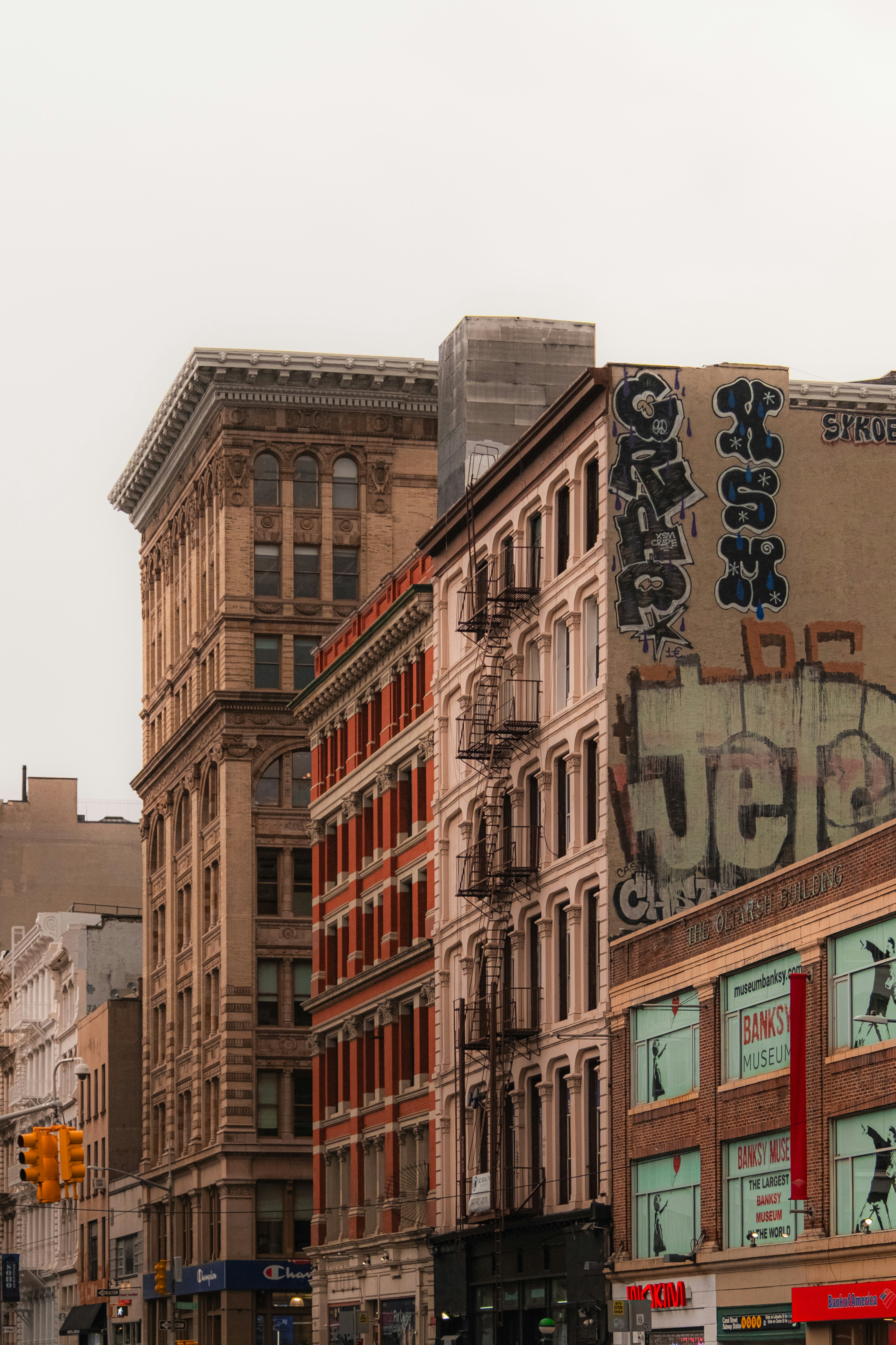 A row of aged urban buildings with varied architectural styles and bold graffiti on the right wall, captured from a street-level perspective; highlights street-level textures and colorful facades.