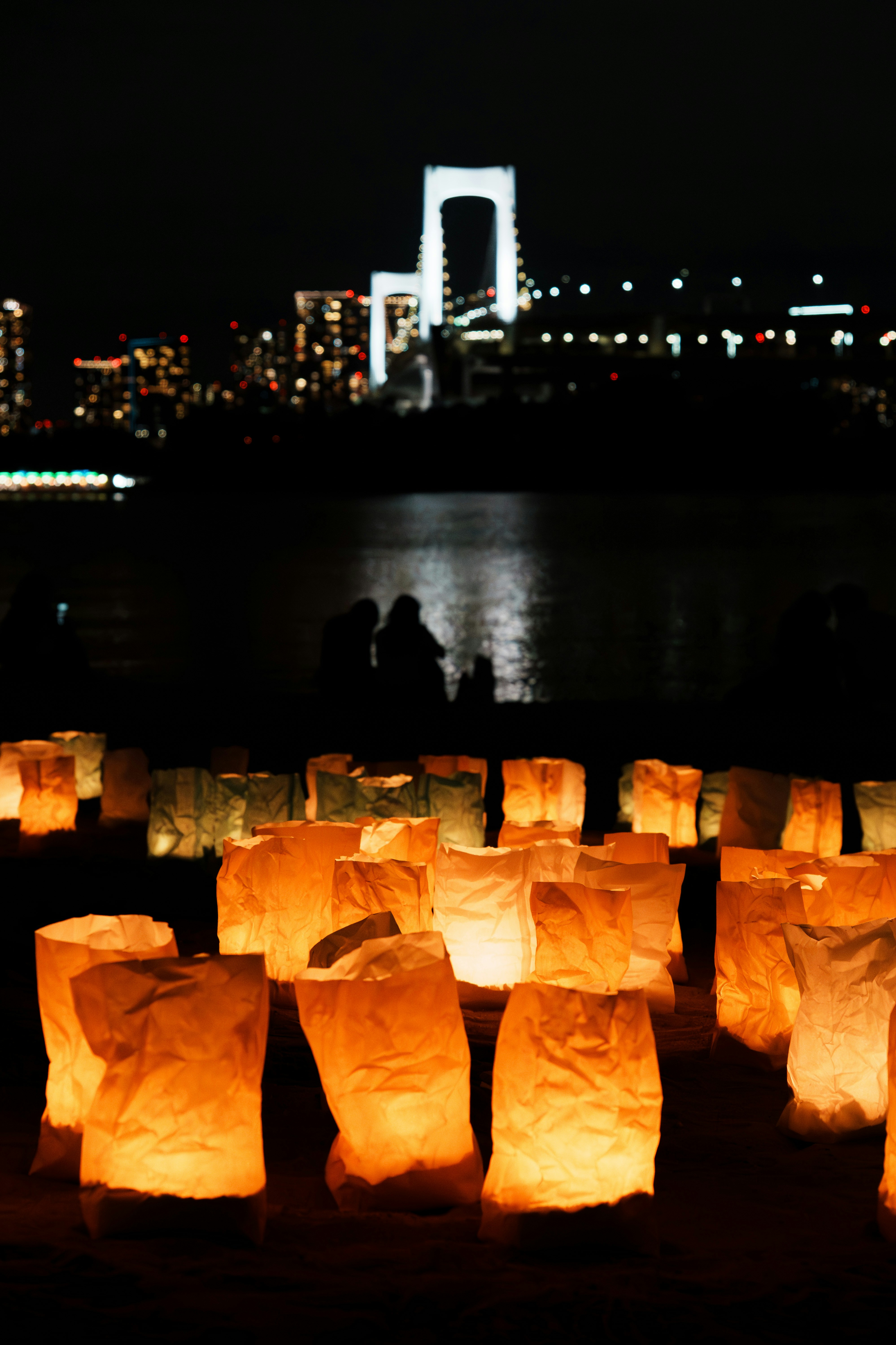 Glowing paper lanterns on a beach at night with the Rainbow Bridge in Tokyo in the background