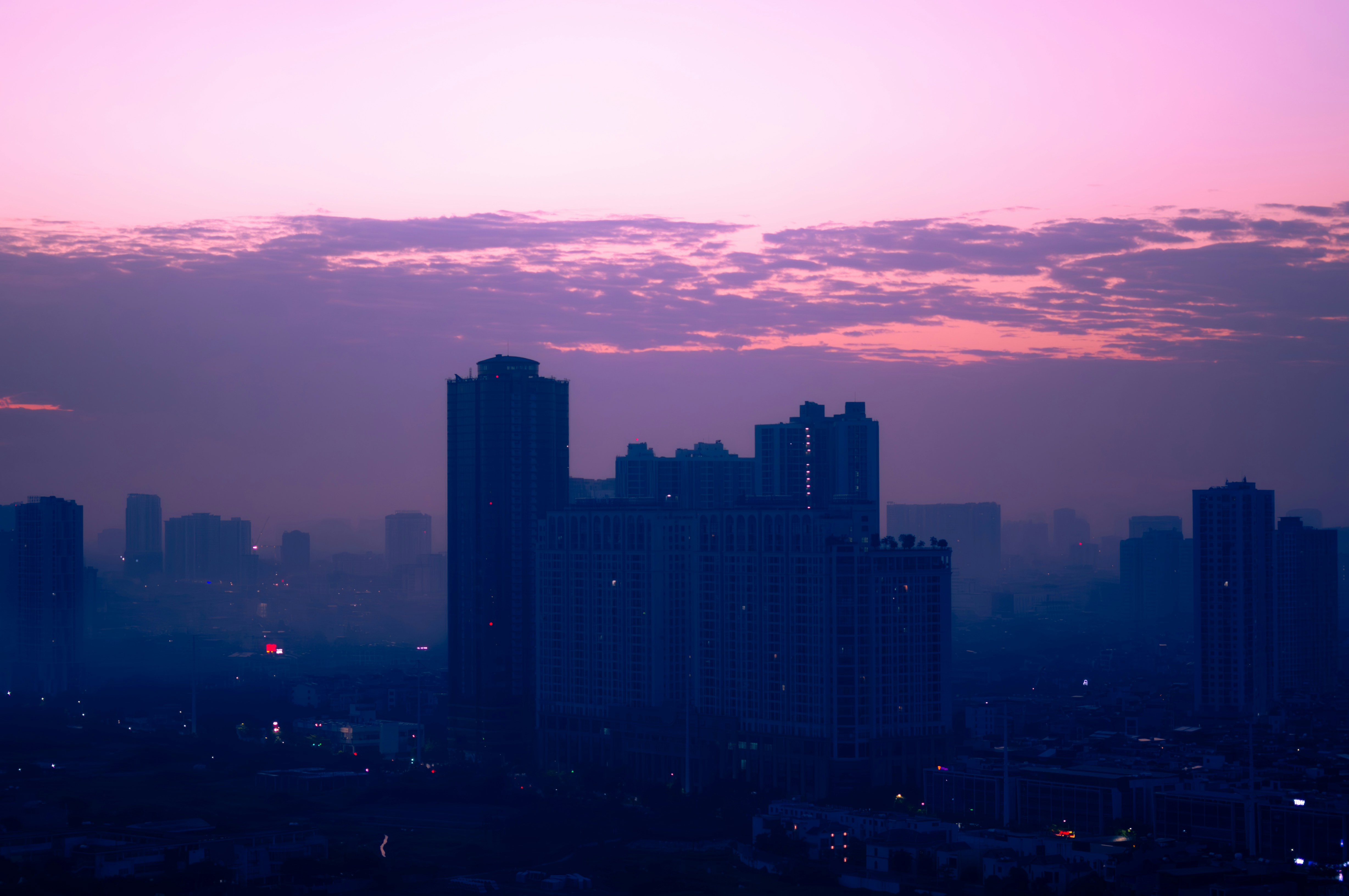 Hazy city skyline at dusk with soft pink sky and silhouetted high-rises, a serene urban horizon.