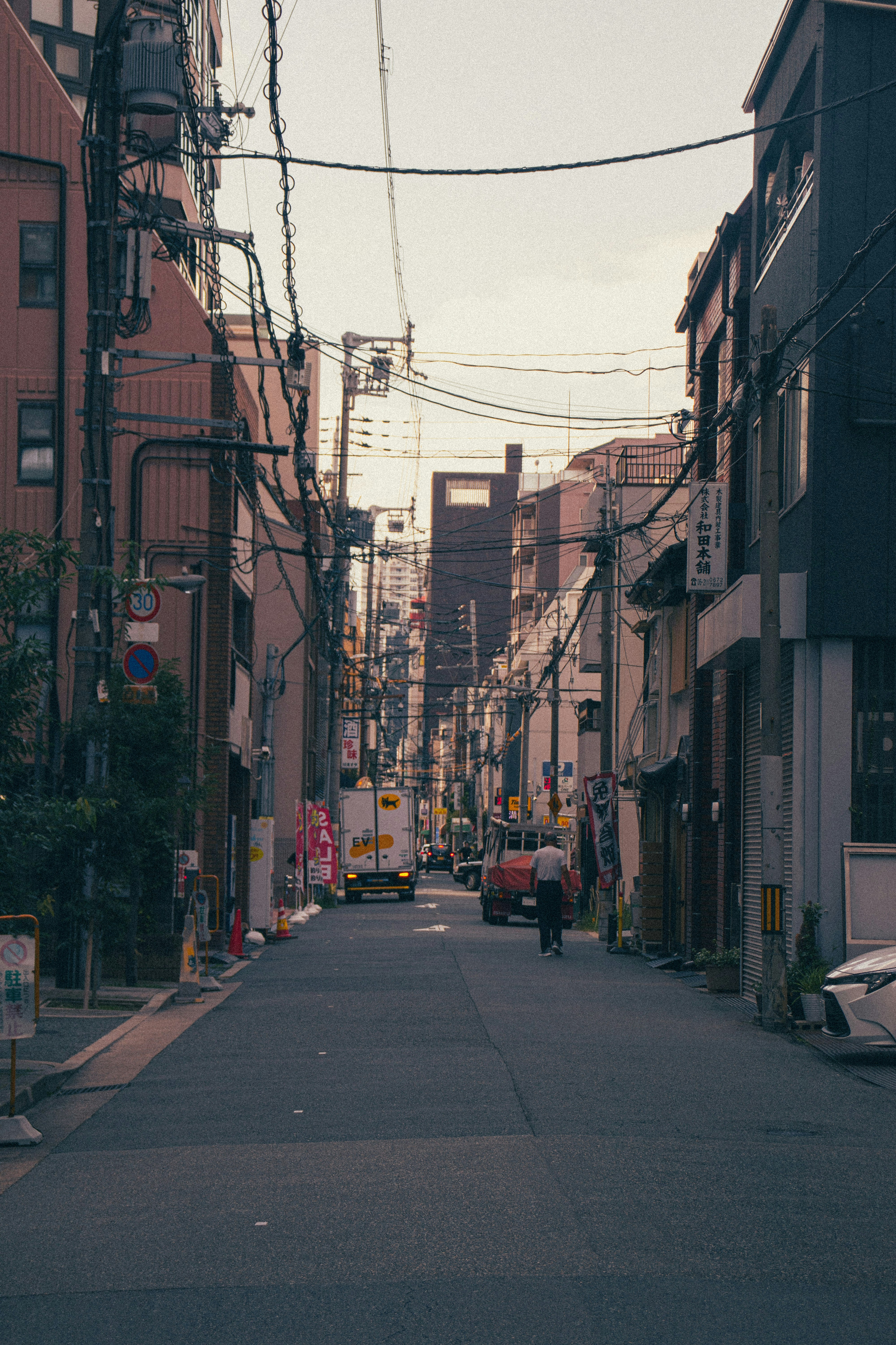 A person walking down a narrow street in Japan lined with buildings and overhead power lines