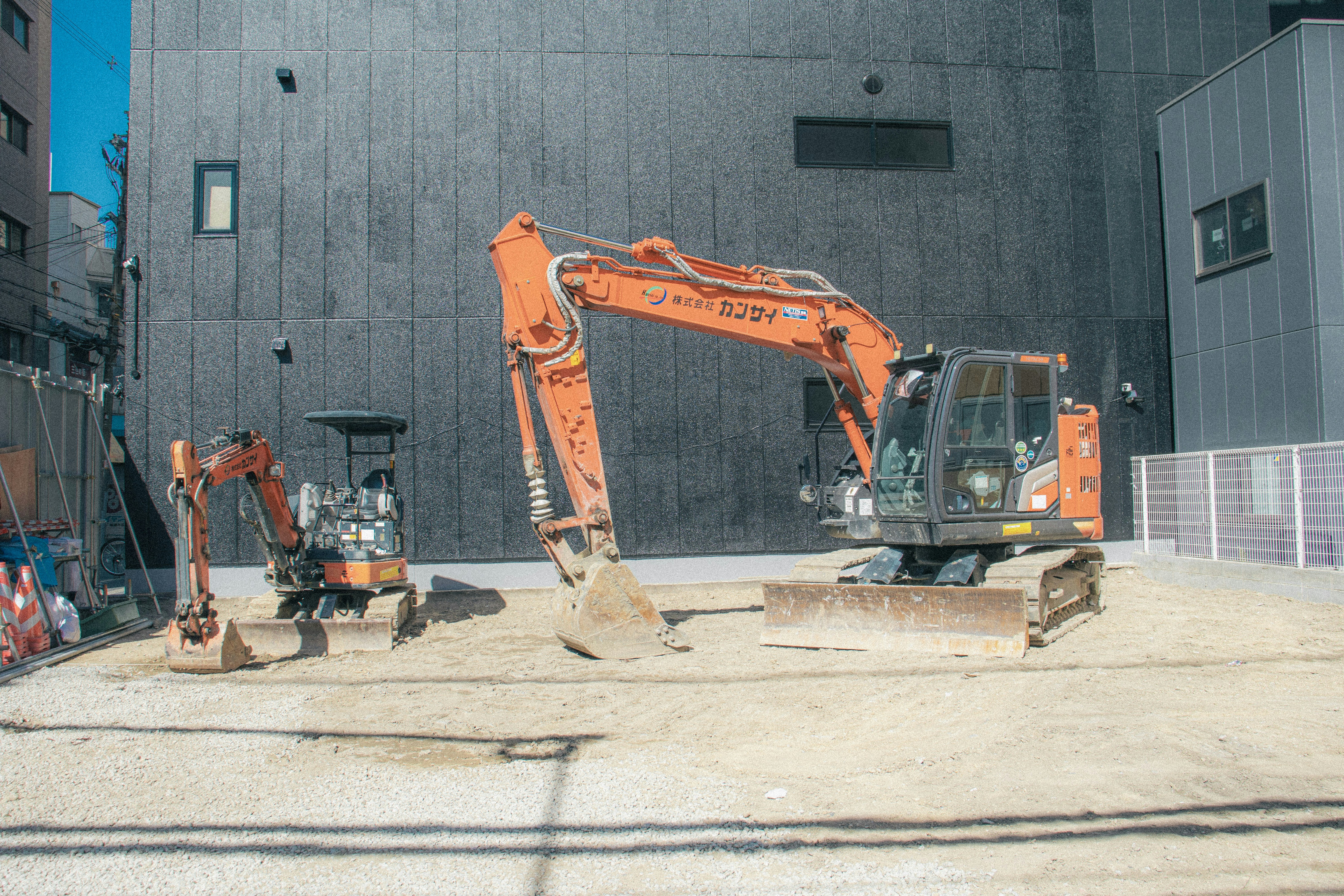 Industrial Echo: Orange Excavators Beneath a Grey Warehouse