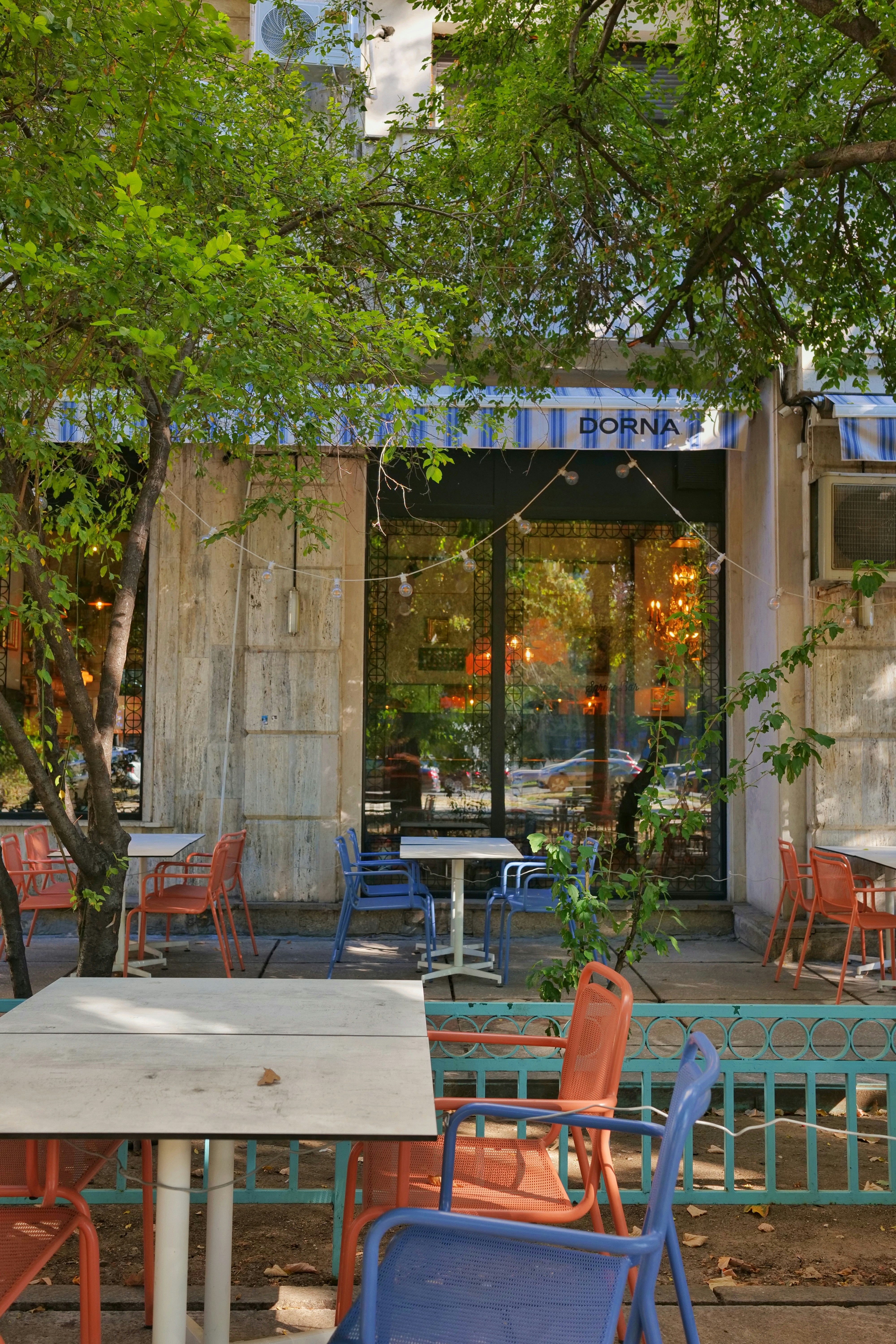 Sunlit Café Terrace Under Green Canopy on a Quiet Street