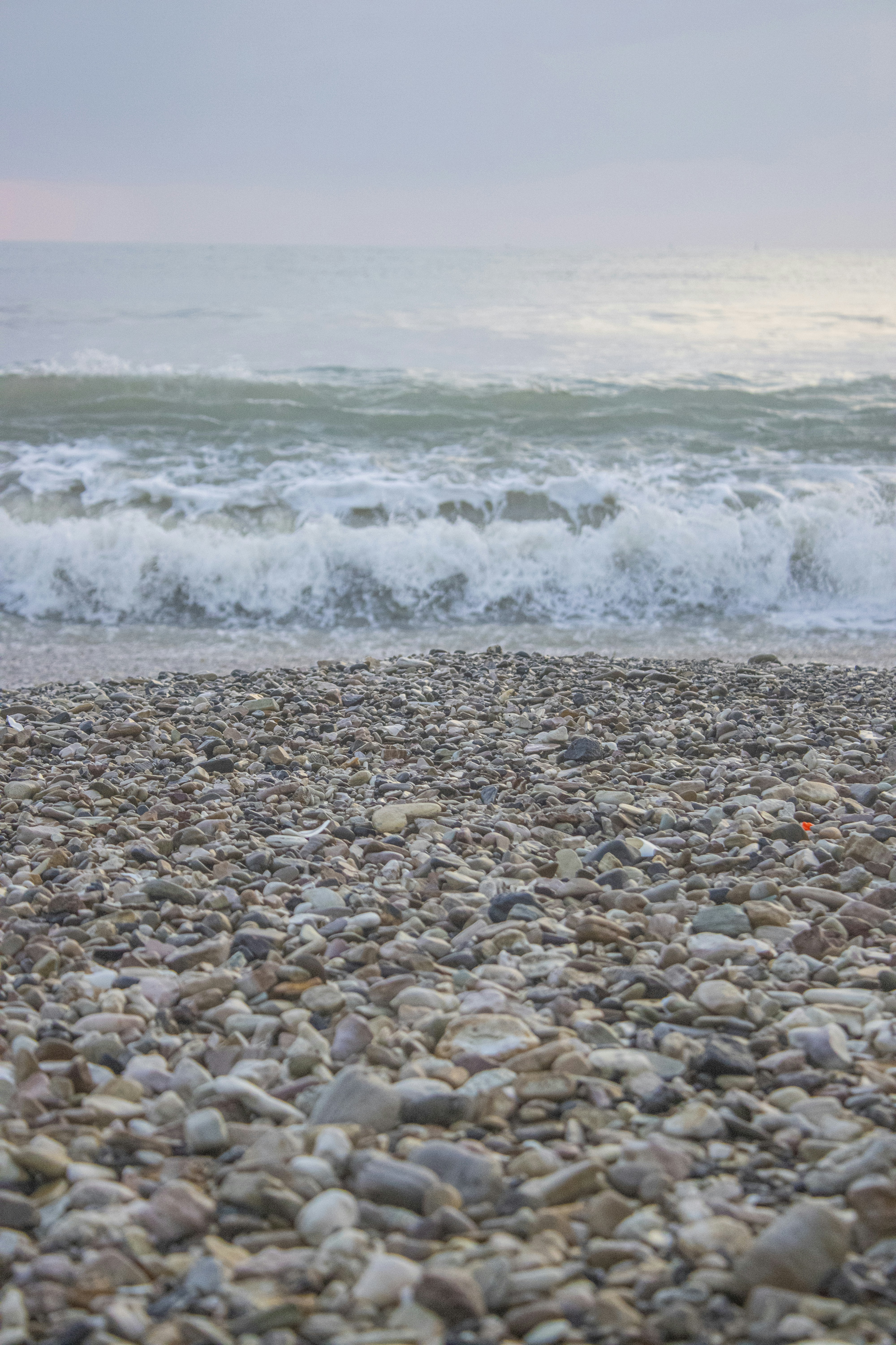 Pebble beach with shorebreak and gentle sea at horizon; a calm seascape capturing textured stones and soft waves. The scene presents landscape texture rather than a person or logo.