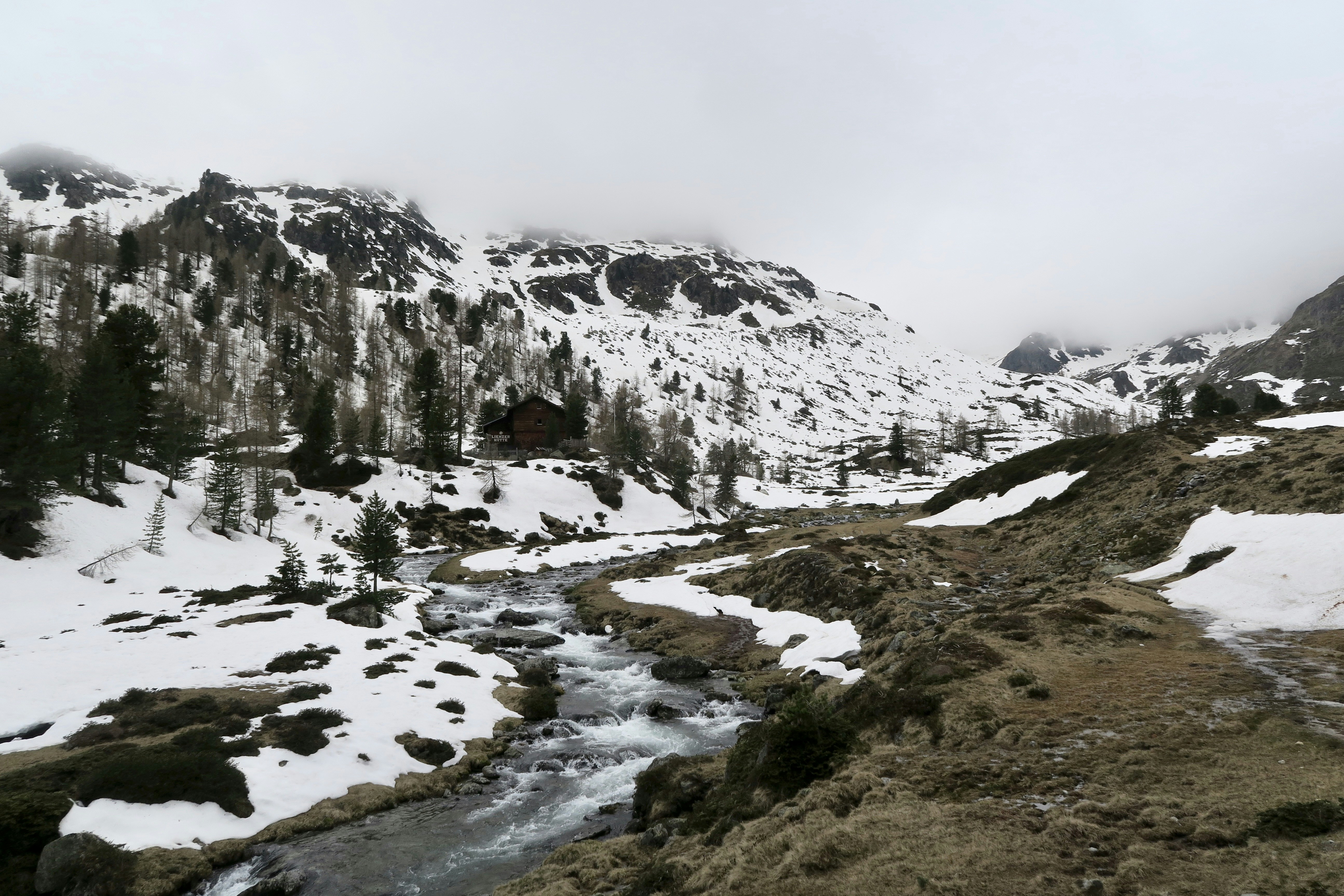 Snow-touched Valley with a Rushing Stream under Clouded Peaks