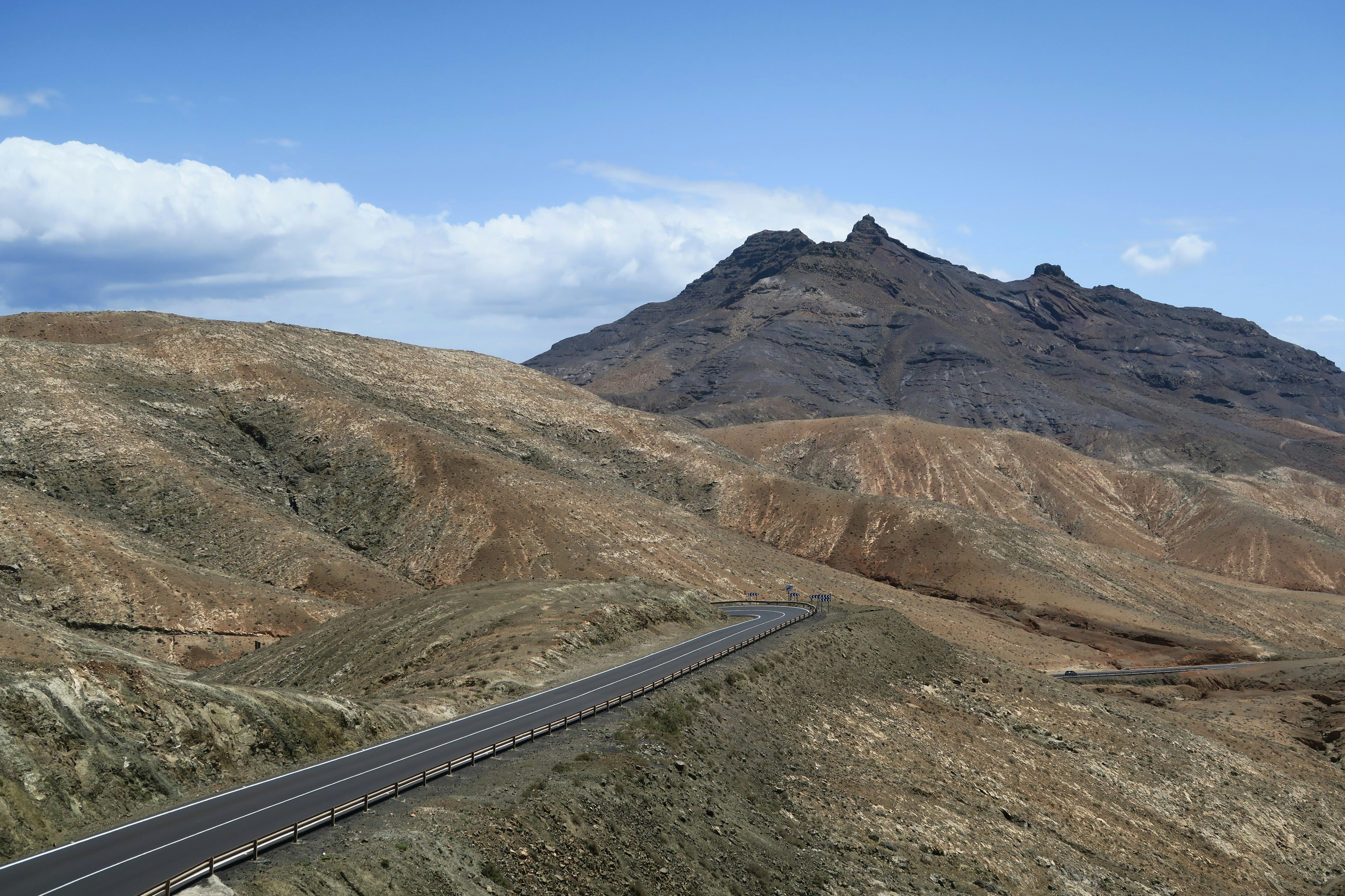 Desert Road Carving Through Rugged Hills Toward a Spired Peak