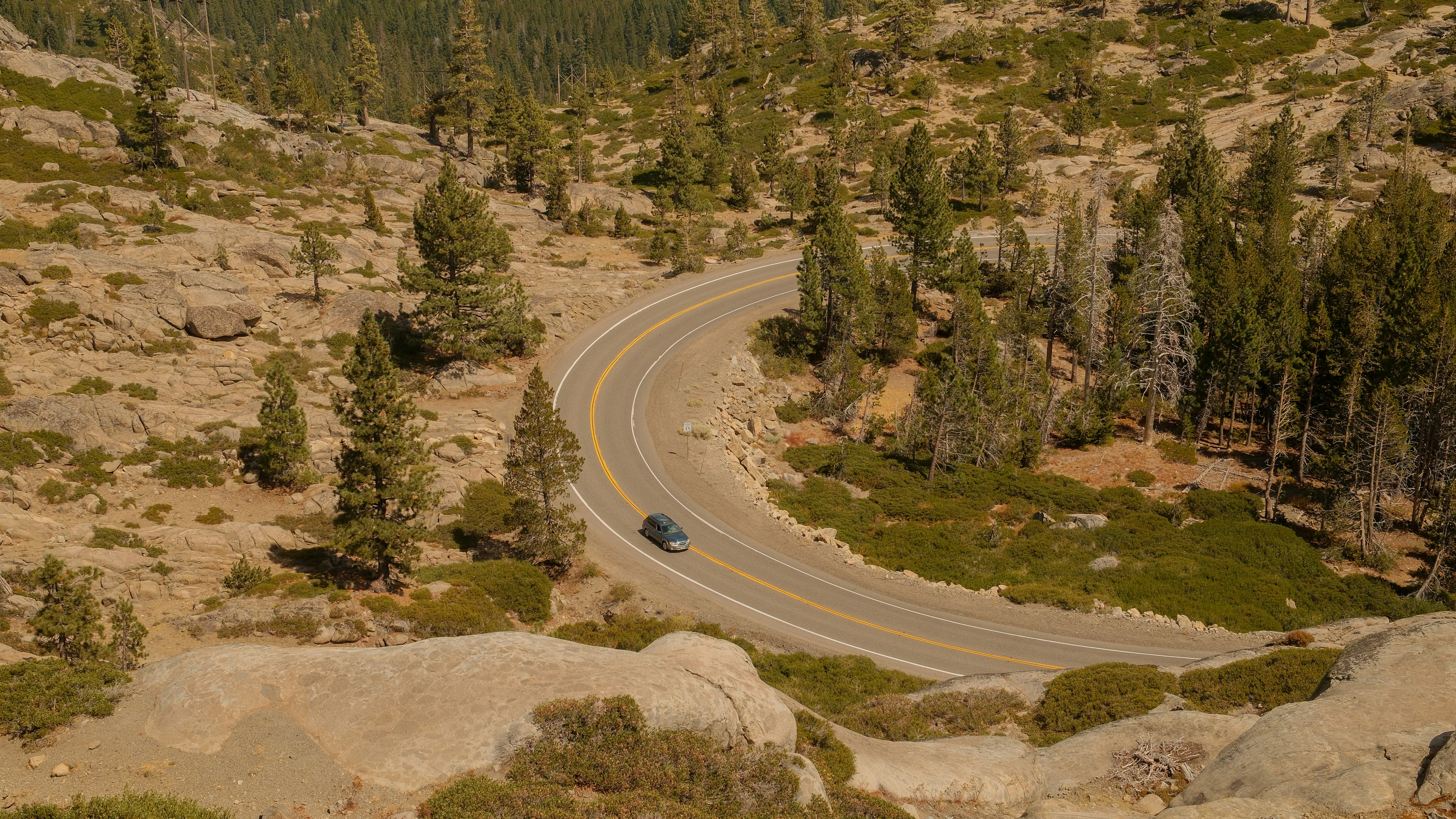 Winding Mountain Road: A solitary car threads the switchbacks through a sunlit pine-strewn hillside