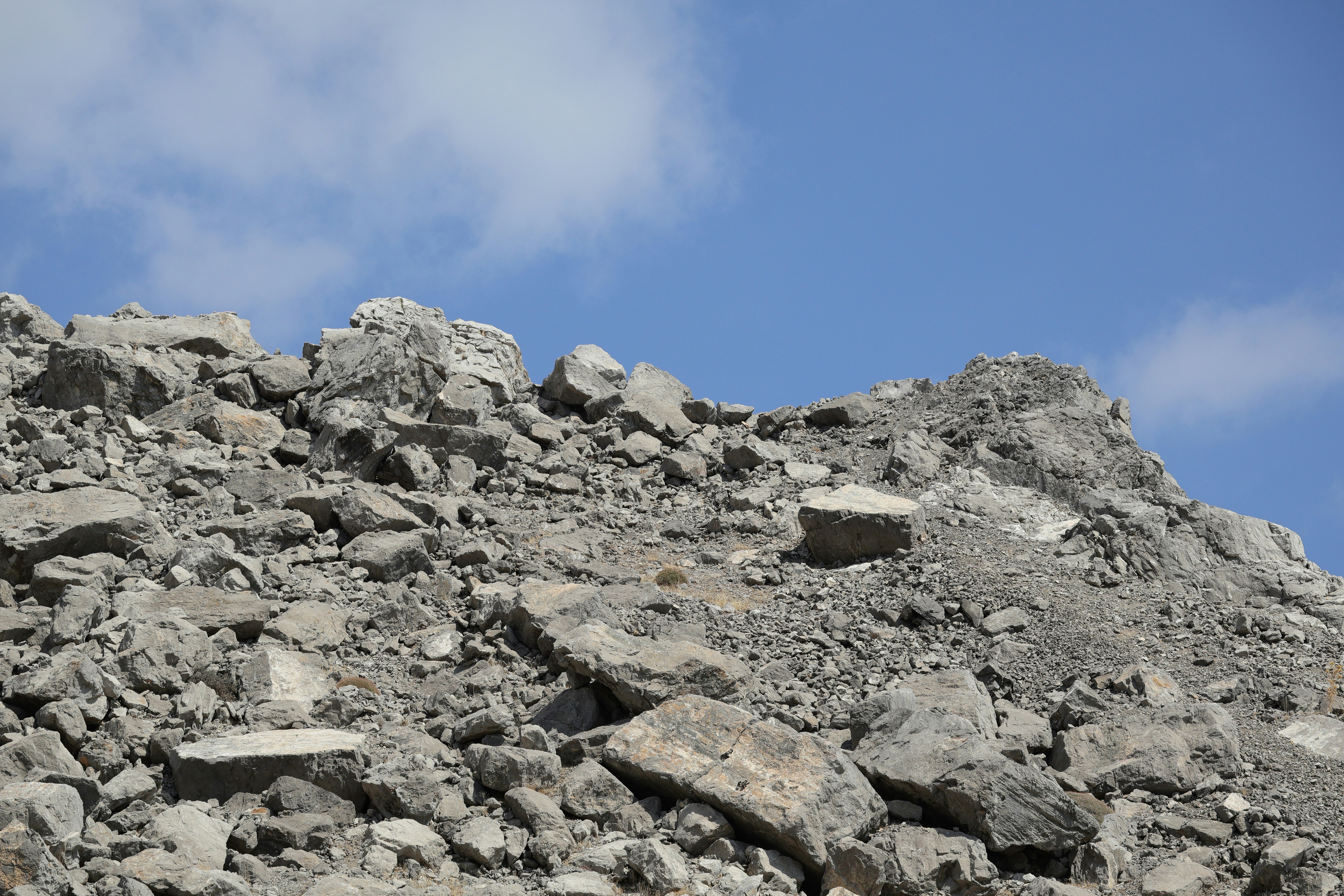 Rough, sunlit scree slopes beneath a bright blue sky with a few clouds; focuses on the texture and arrangement of rocky terrain.