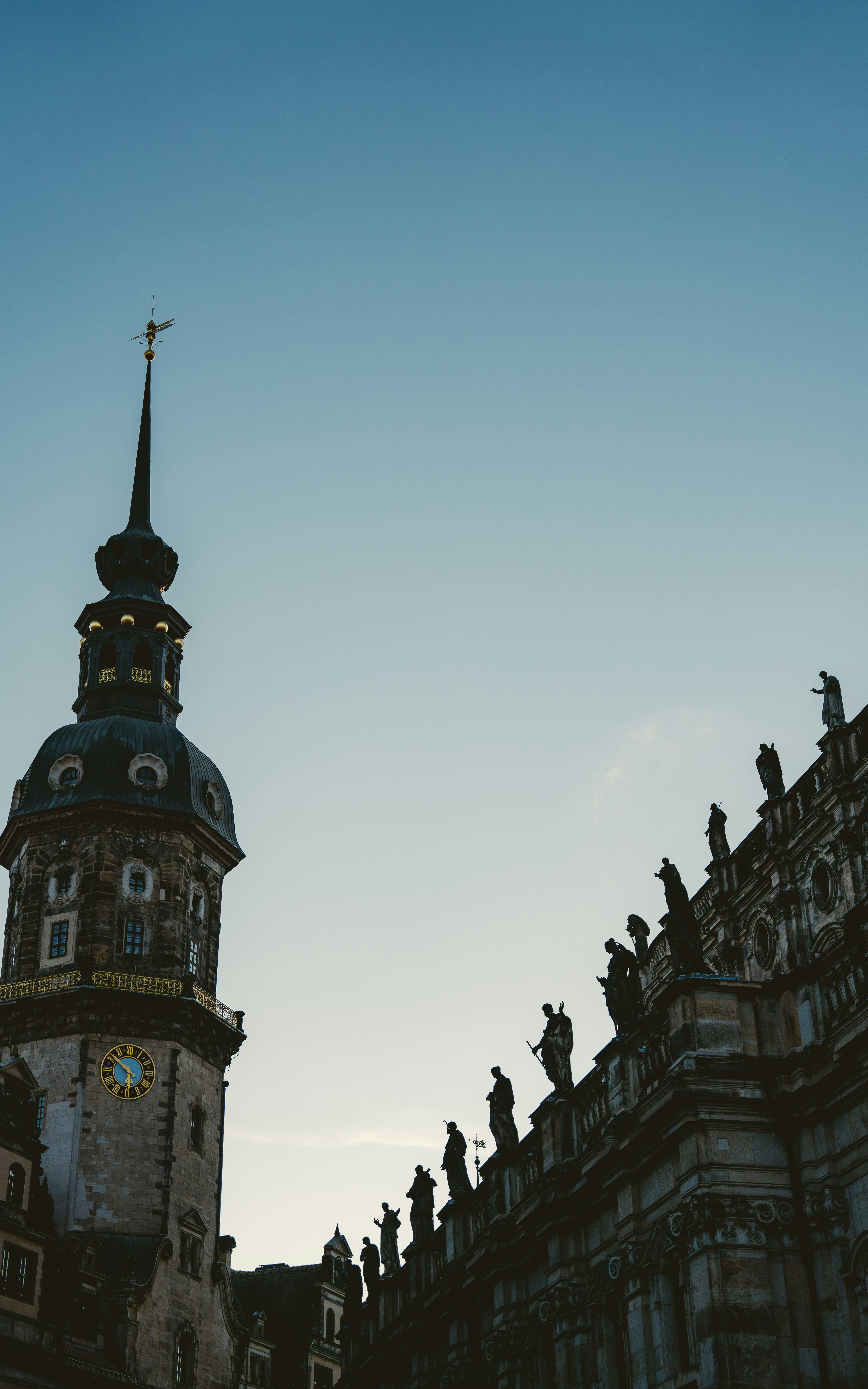 Tall clock tower and ornate roofline silhouette set against a blue sky, emphasizing architectural details and skyline.