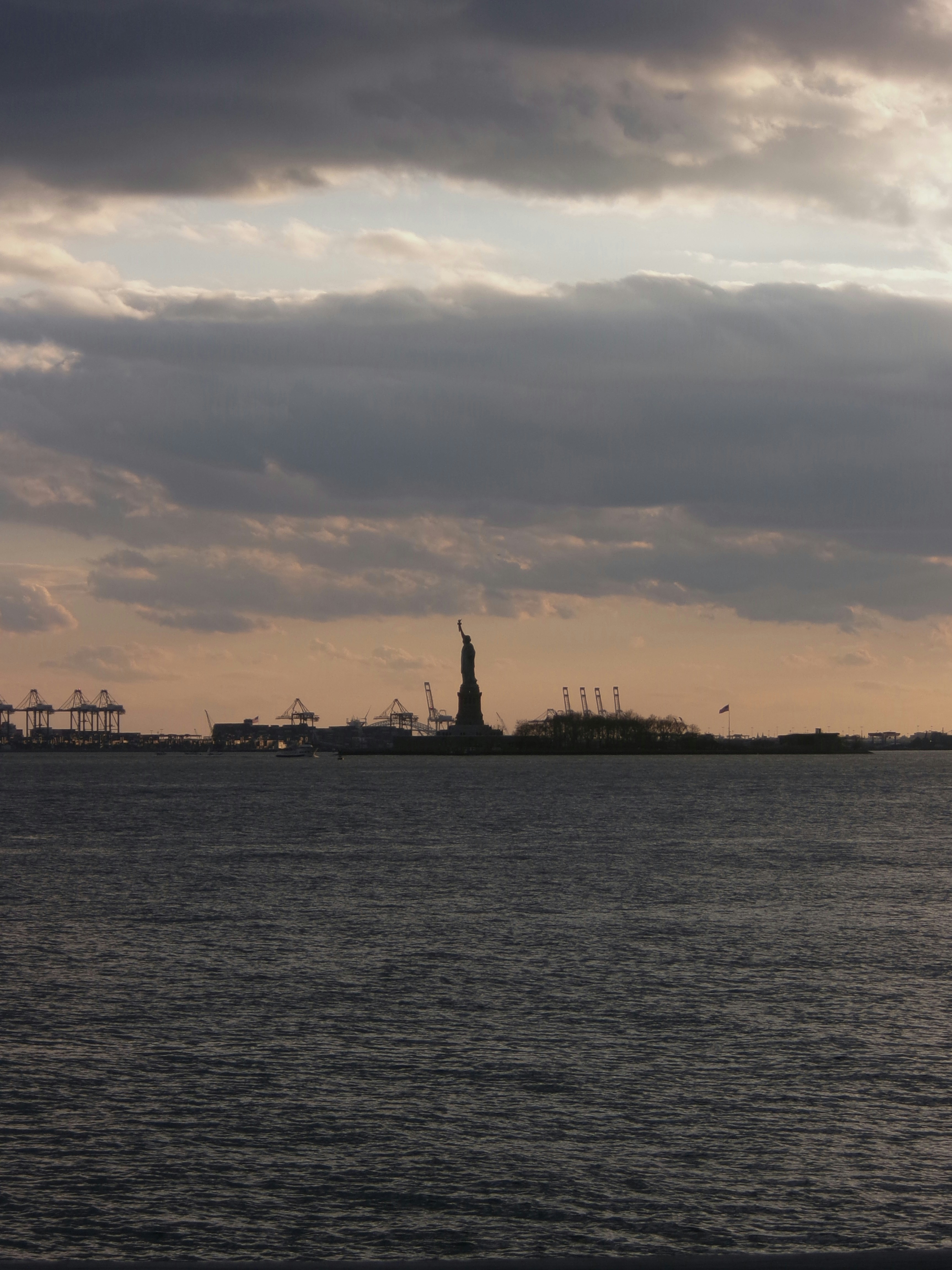 Distant Liberty: silhouette of the Statue of Liberty against a harbor sunset