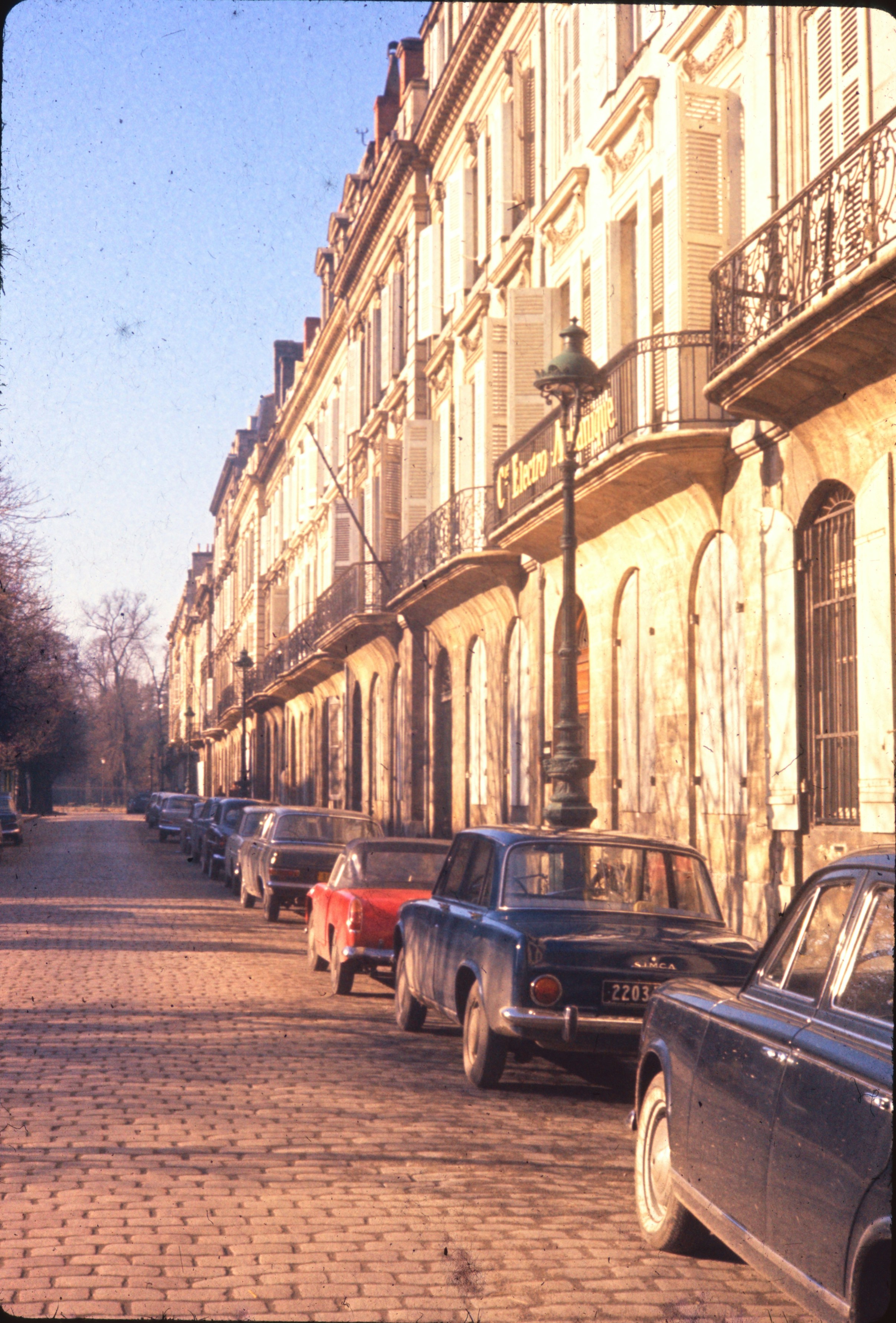 Sunlit Parisian Rue: A Row of Historic Facades and Vintage Cars