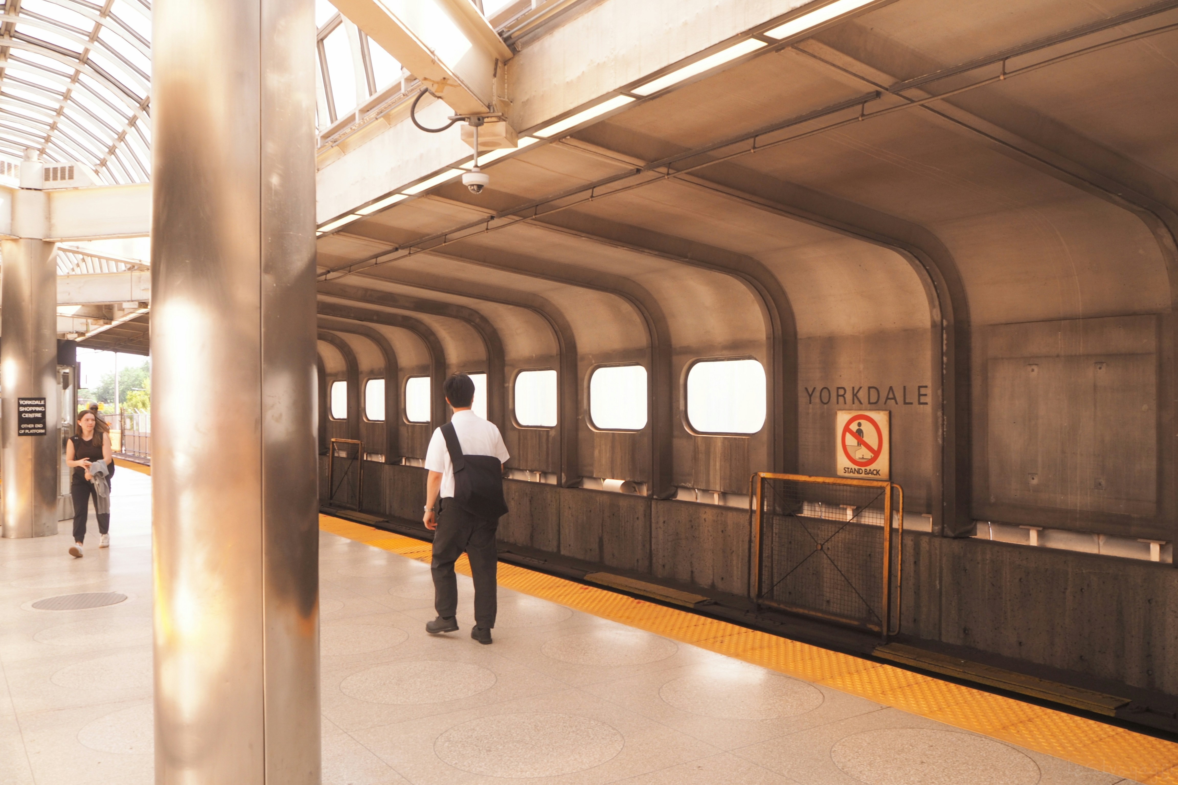  commuter in a sunlit subway platform near the arced, industrial walls