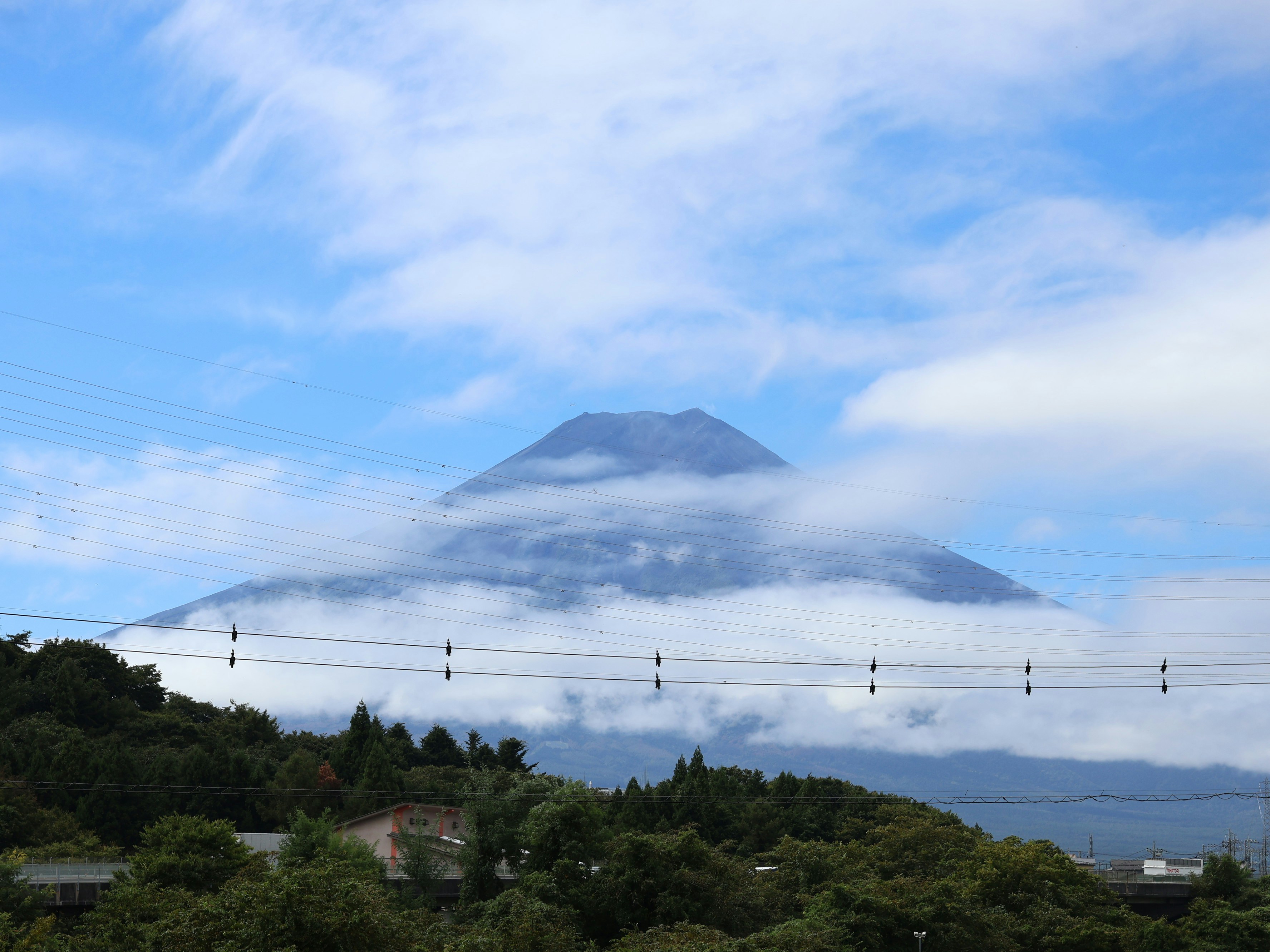 Peak Amid Clouds: A Mountain Rising Above a Line of Trees and Rail Wires