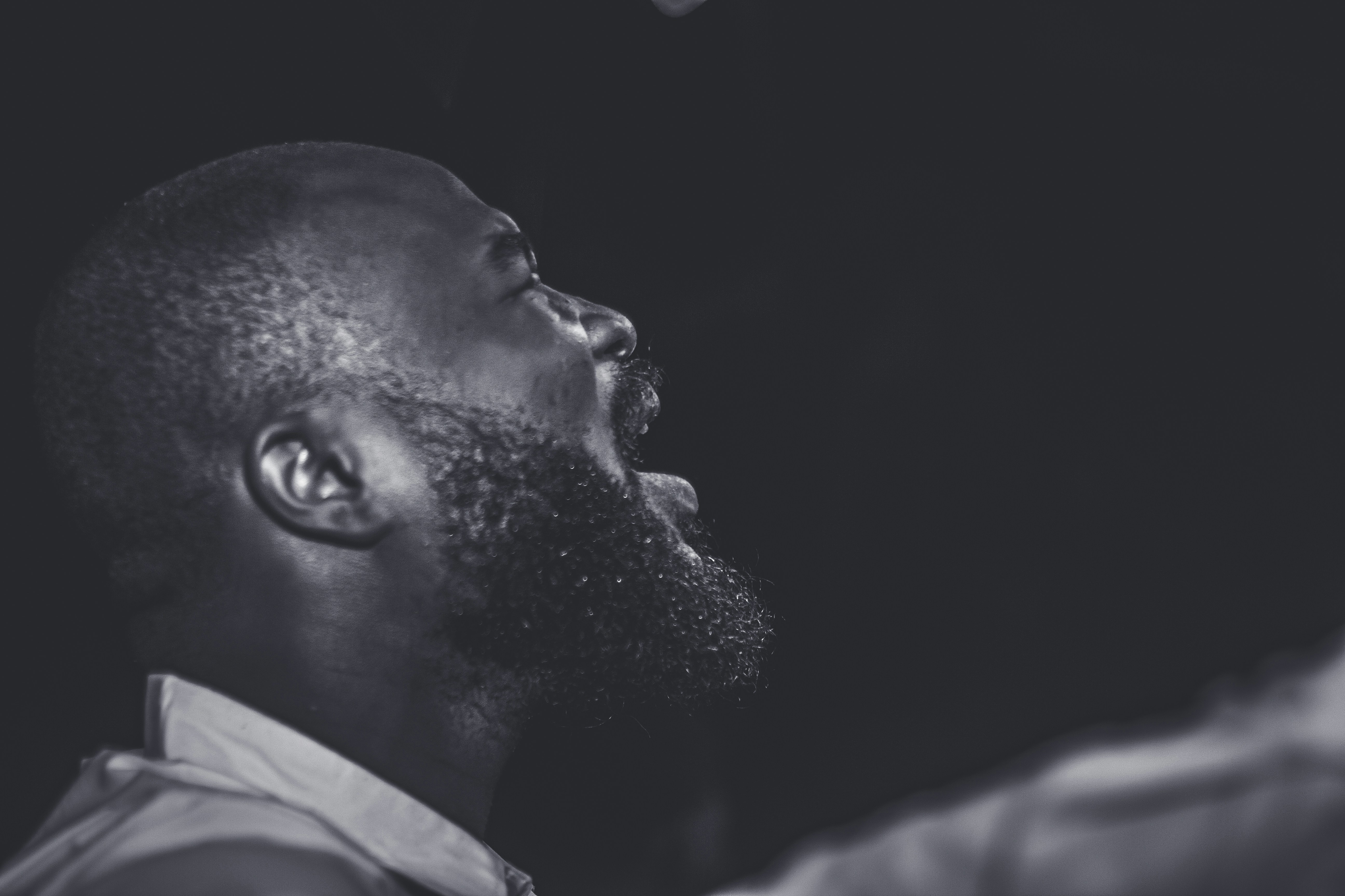 Close-up of a man in profile, eyes closed and mouth slightly open, captured in low light with a shallow depth of field; monochrome rendering emphasizes texture and emotion.