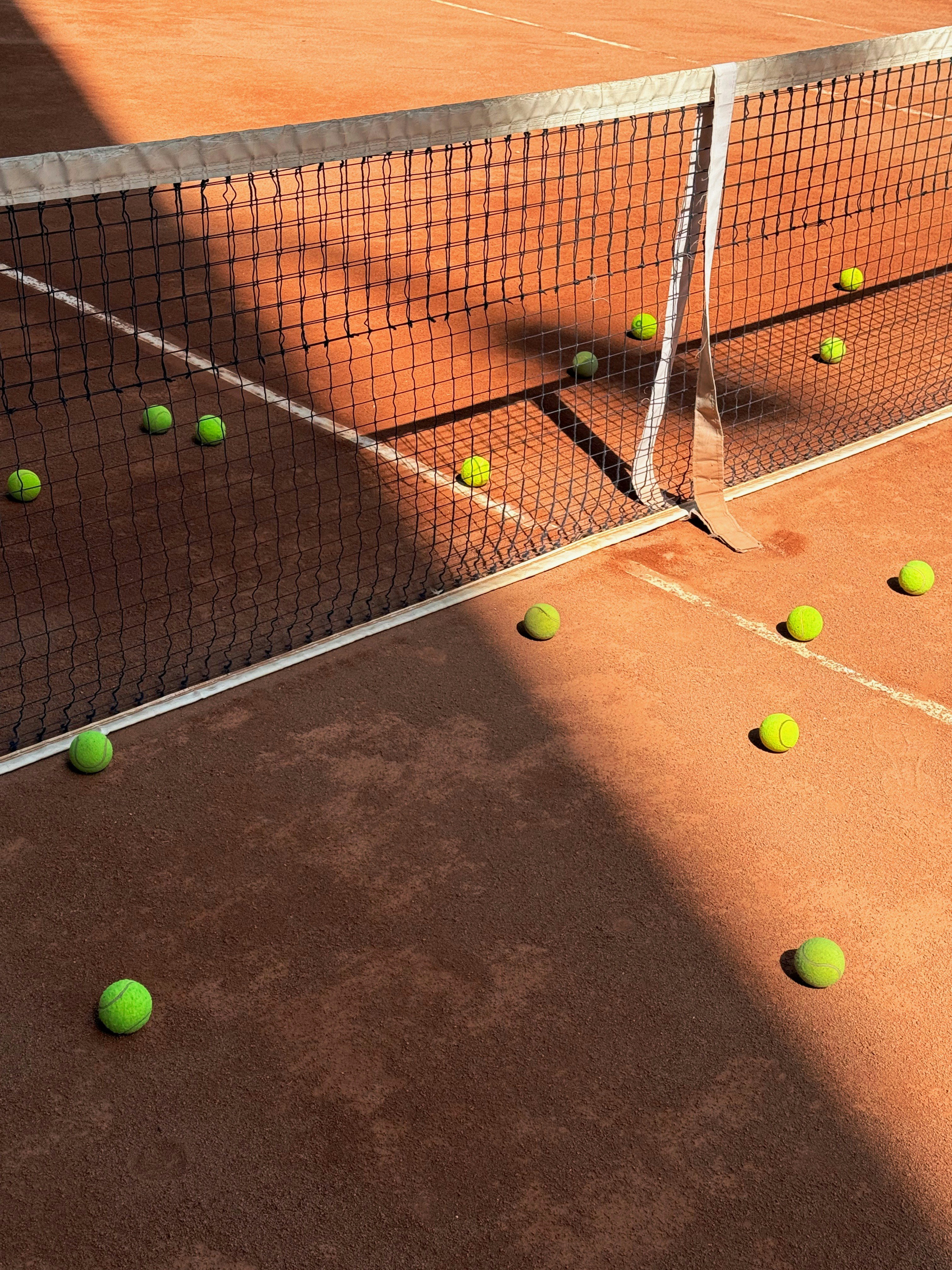 Sunlit Tennis Court: Scatter of Yellow Balls and a Drooping Net Shadow