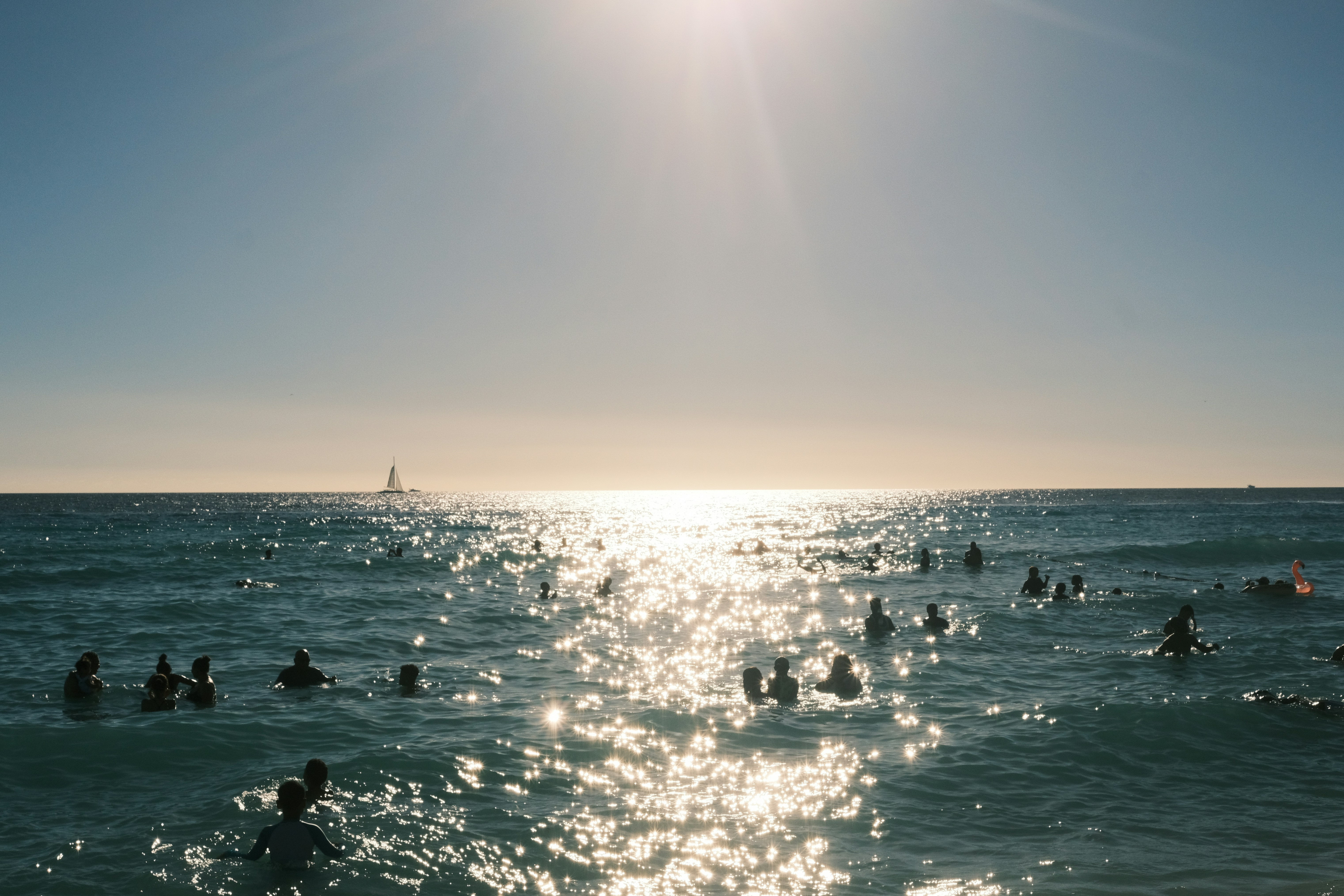 Sunlit Ocean Crowds: Glinting Waves and Distant Sail