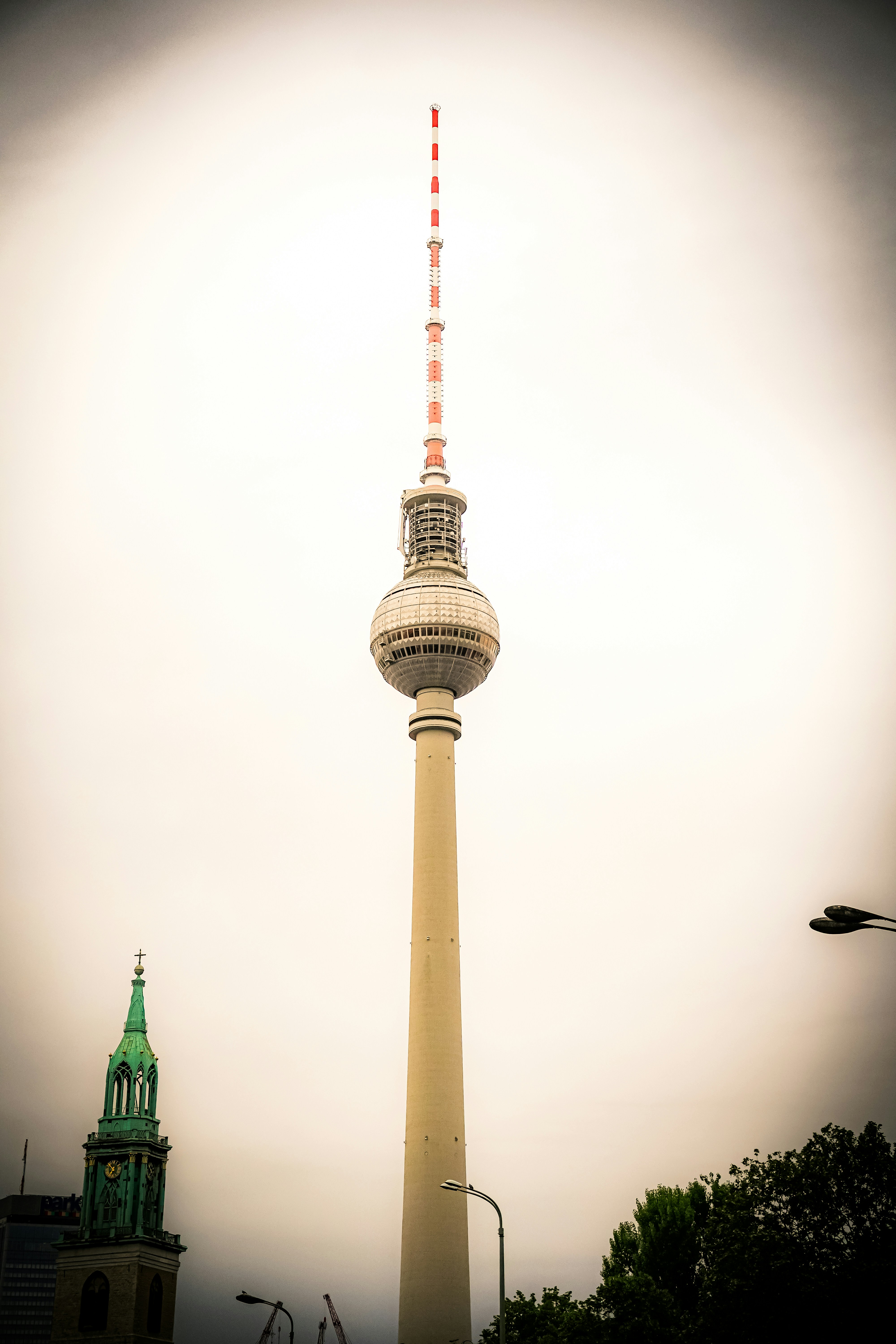 Spire Above the City: a tall view of Berlin’s Fernsehturm framed by a green church steeple