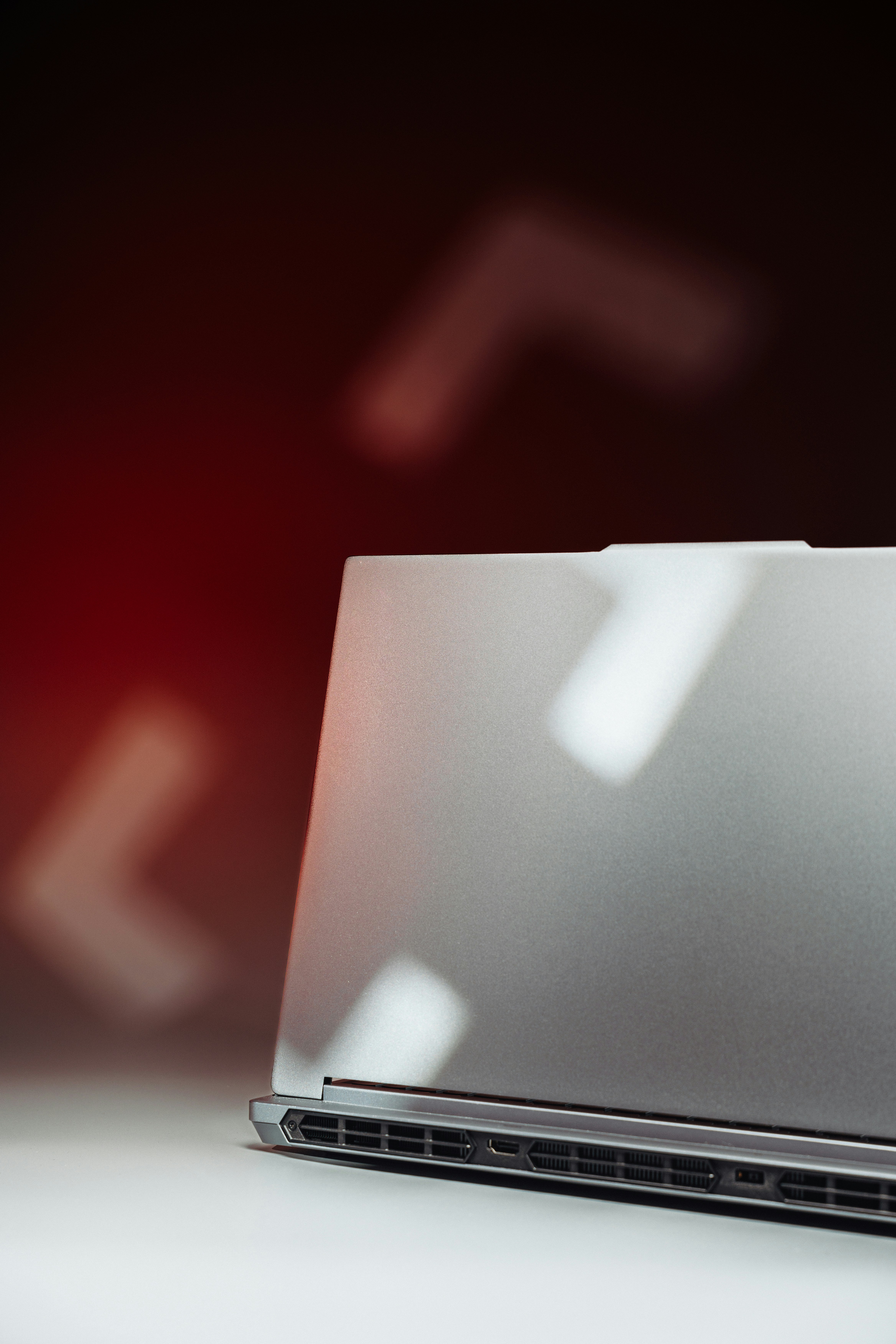 Silver laptop silhouette under soft studio glow with abstract red light trails