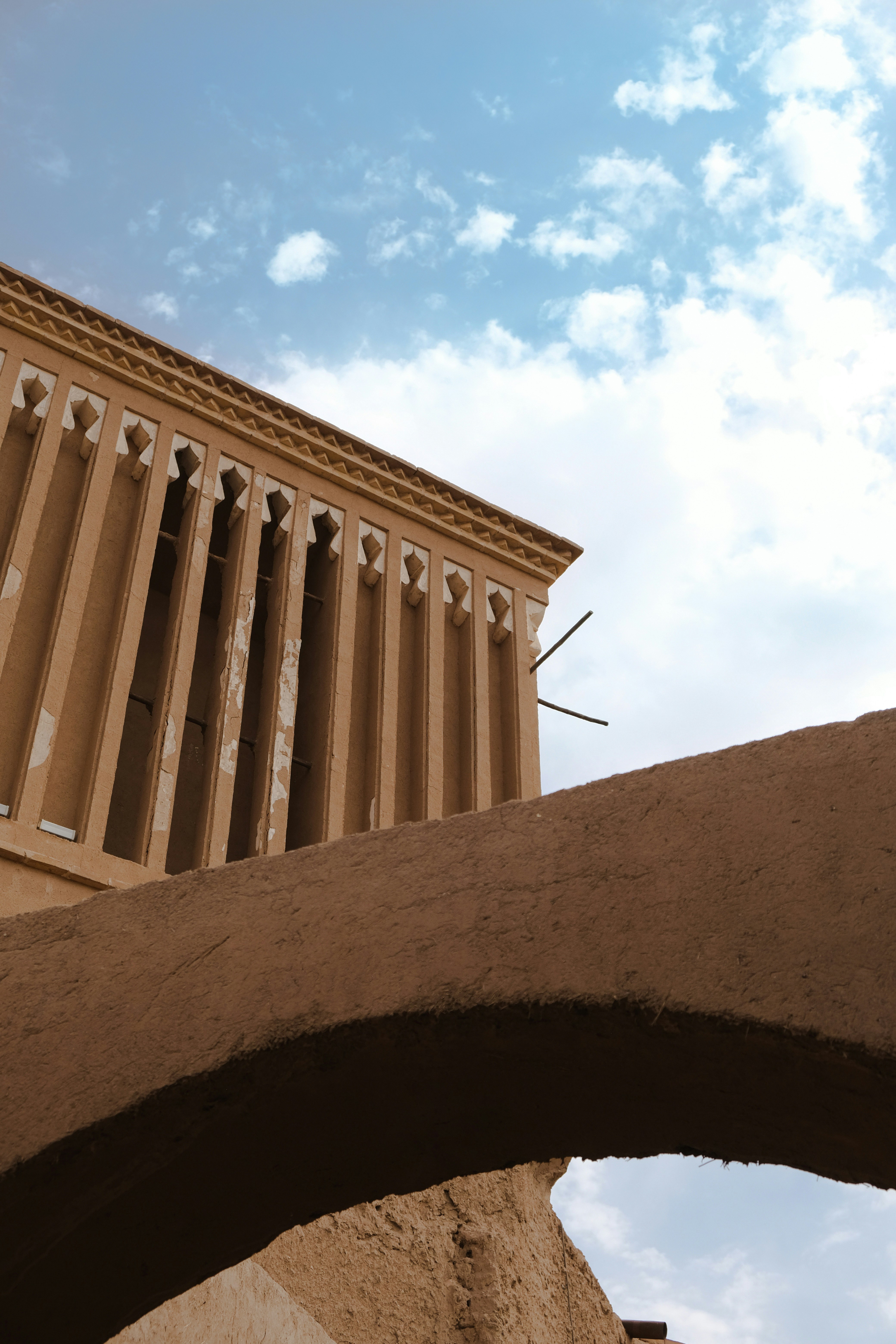 Desert architectural facade with carved columns and a weathered arch under a blue sky, emphasizing textures and a diagonal composition.