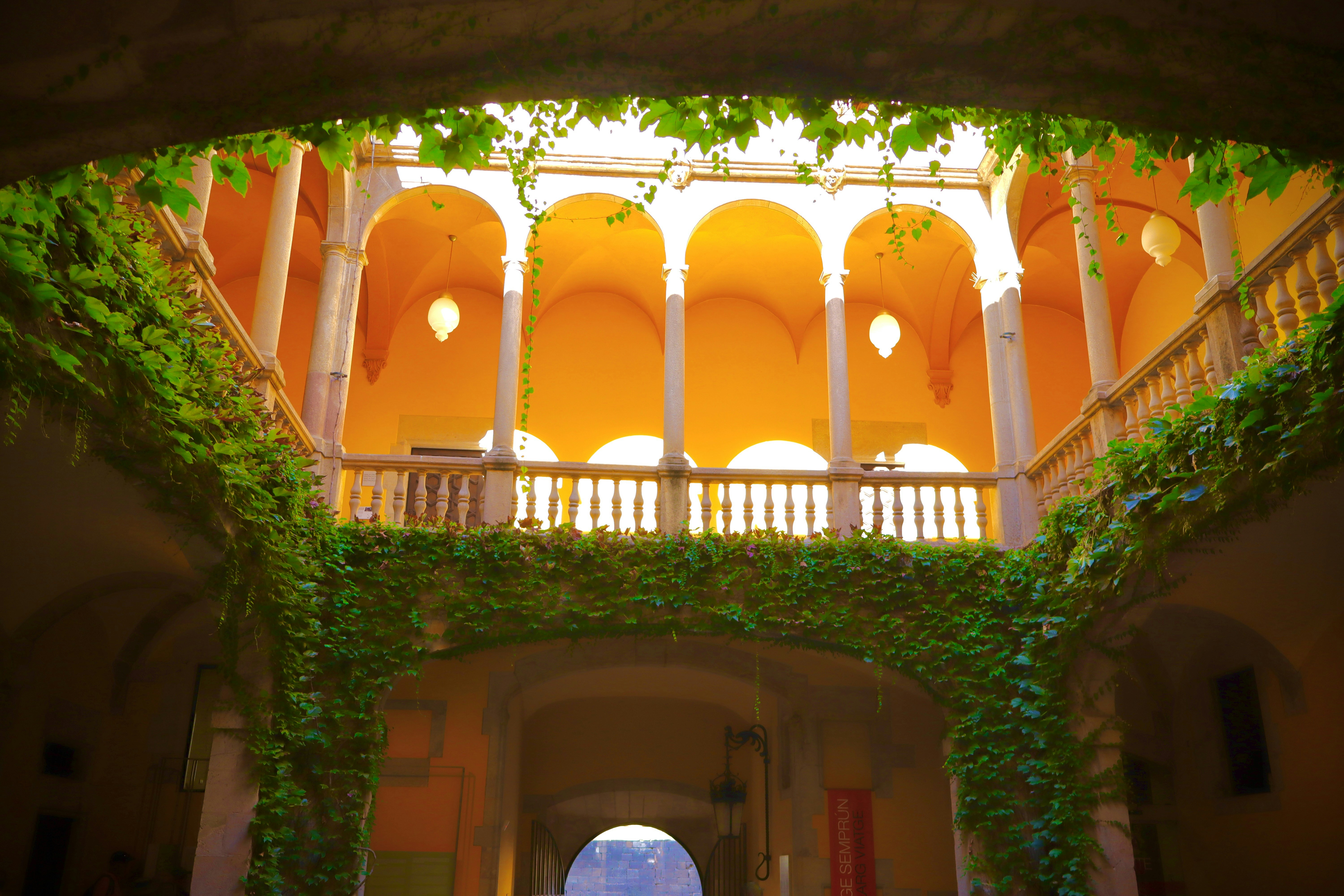 Warm courtyard arches bathed in amber light, with ivy-clad walls and a blue circular opening at ground level.