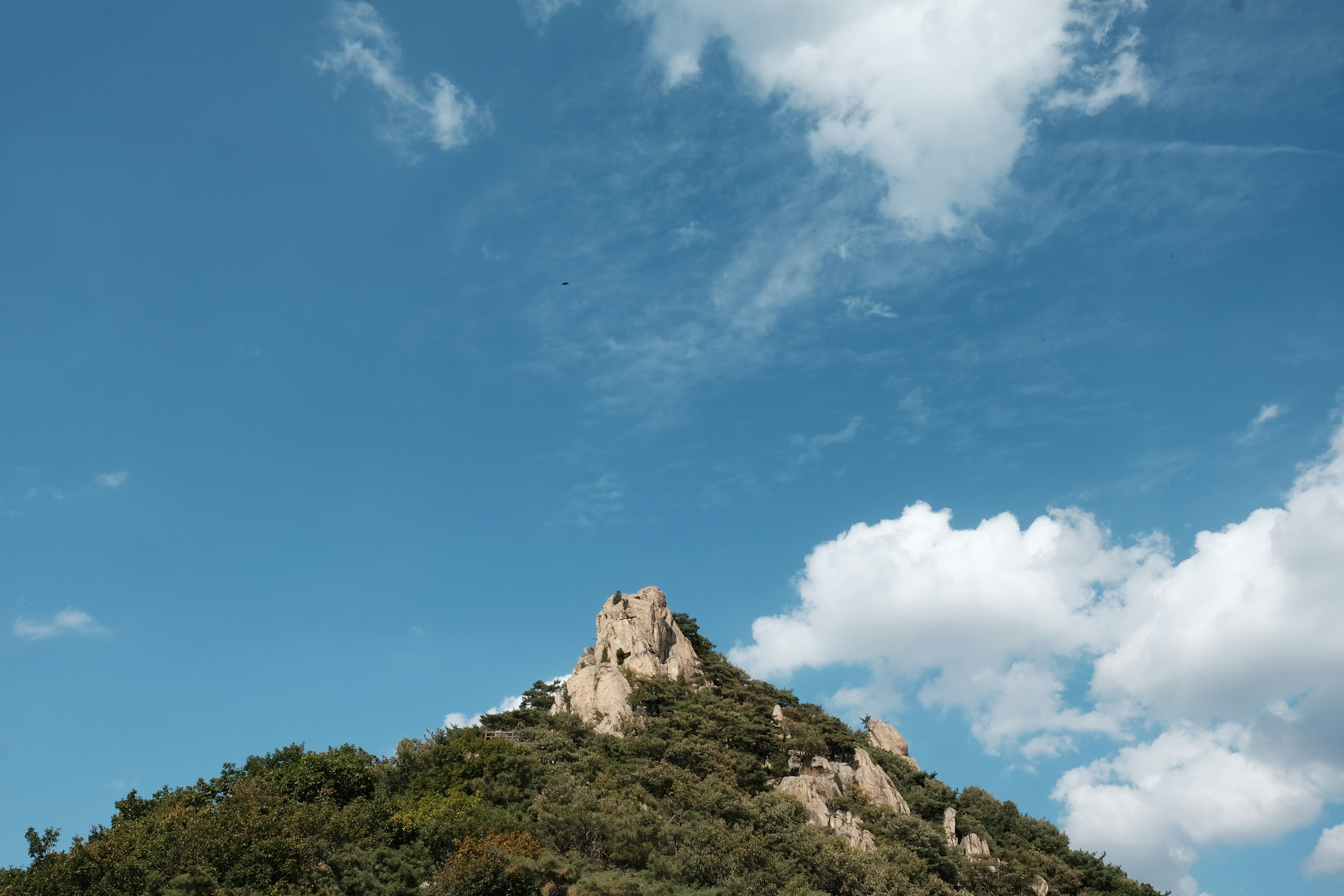 Verdant hill crowned with a rugged rock formation beneath a bright blue sky, capturing a solitary landmark against rolling greenery.