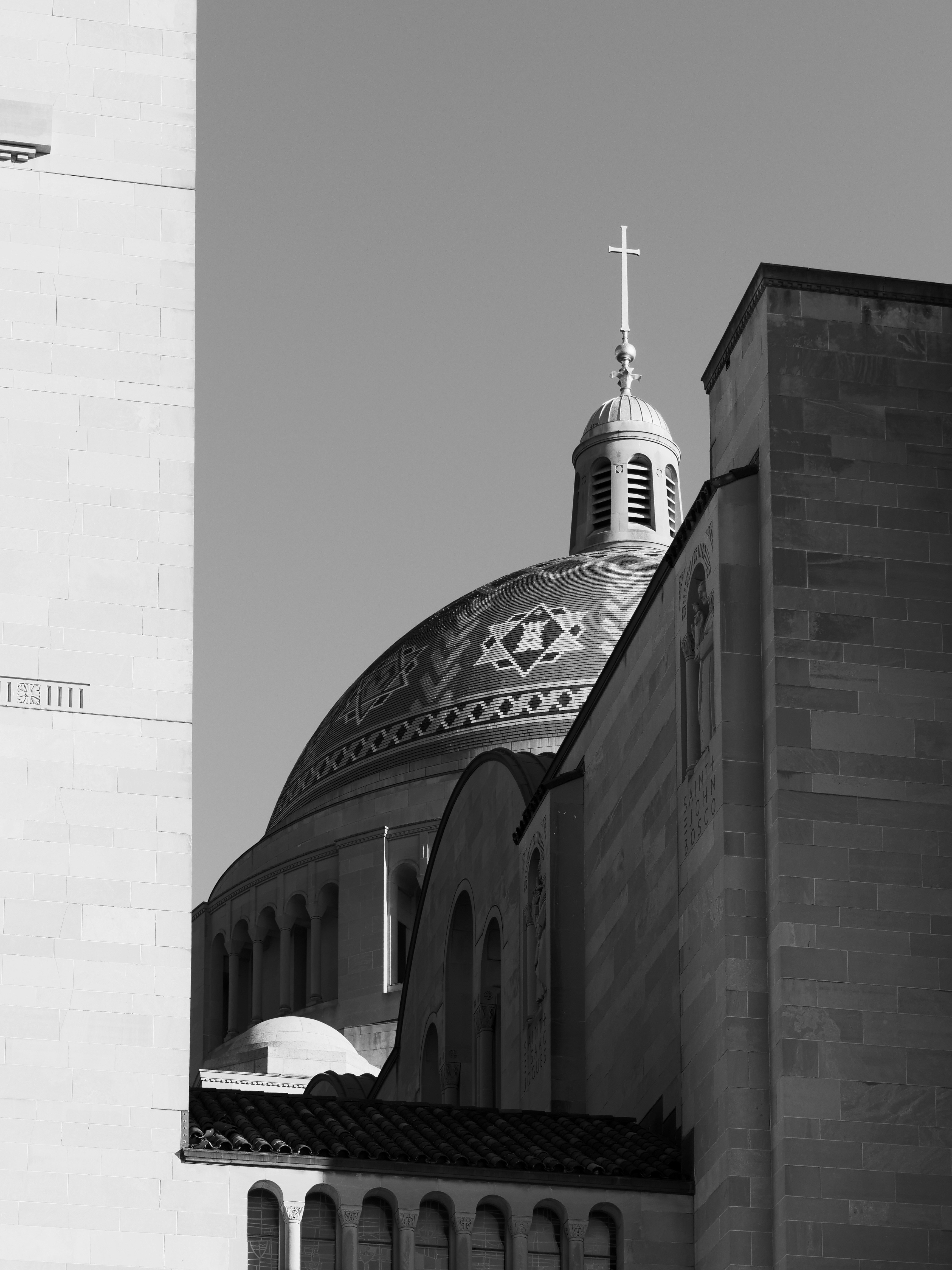 Monochrome view of a domed roof with a cross, framed between architectural walls, highlighting geometric contrast and religious symbolism.