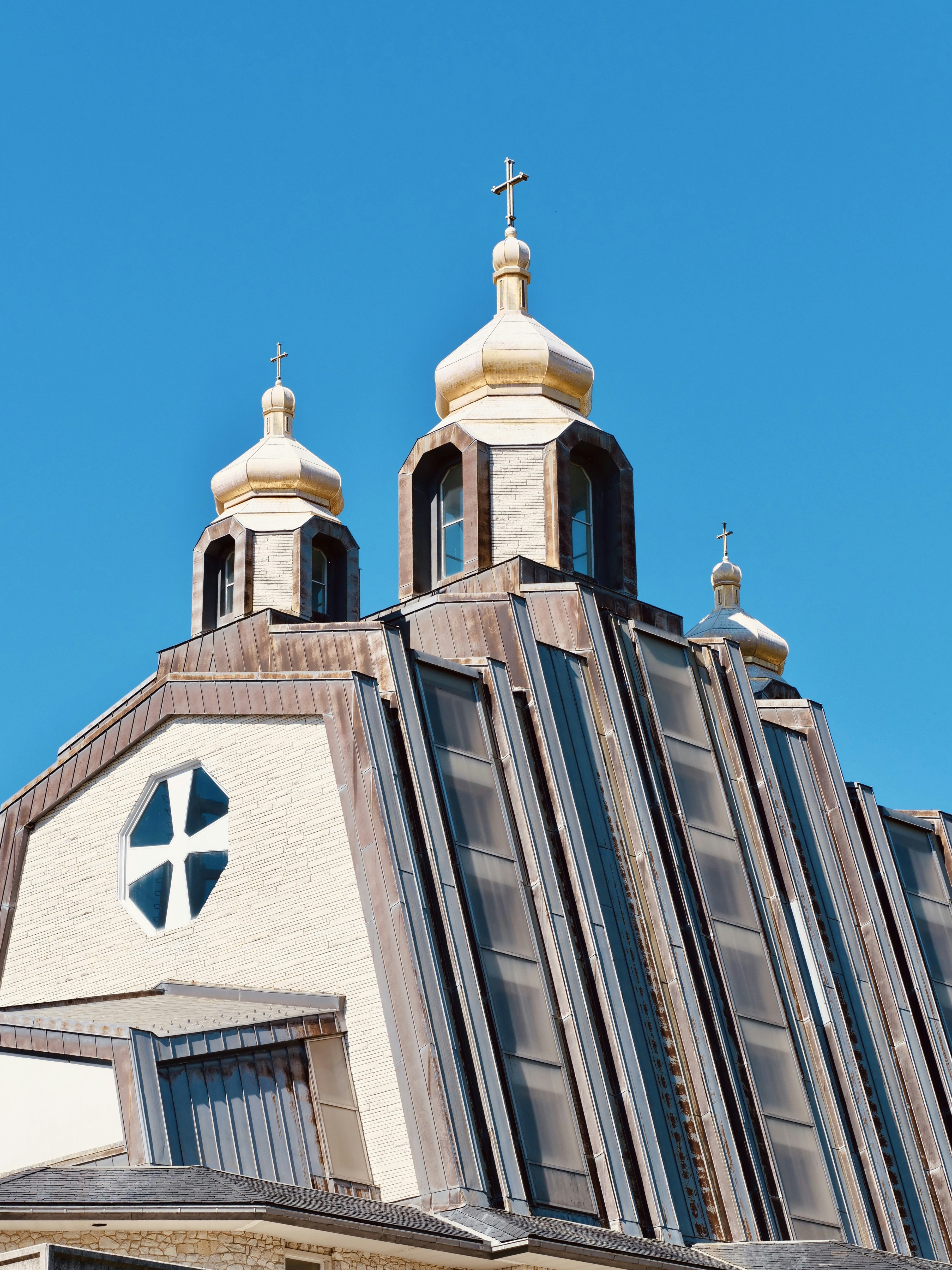 Architectural detail of a church roof with three gold domes and cross finials under a clear blue sky.