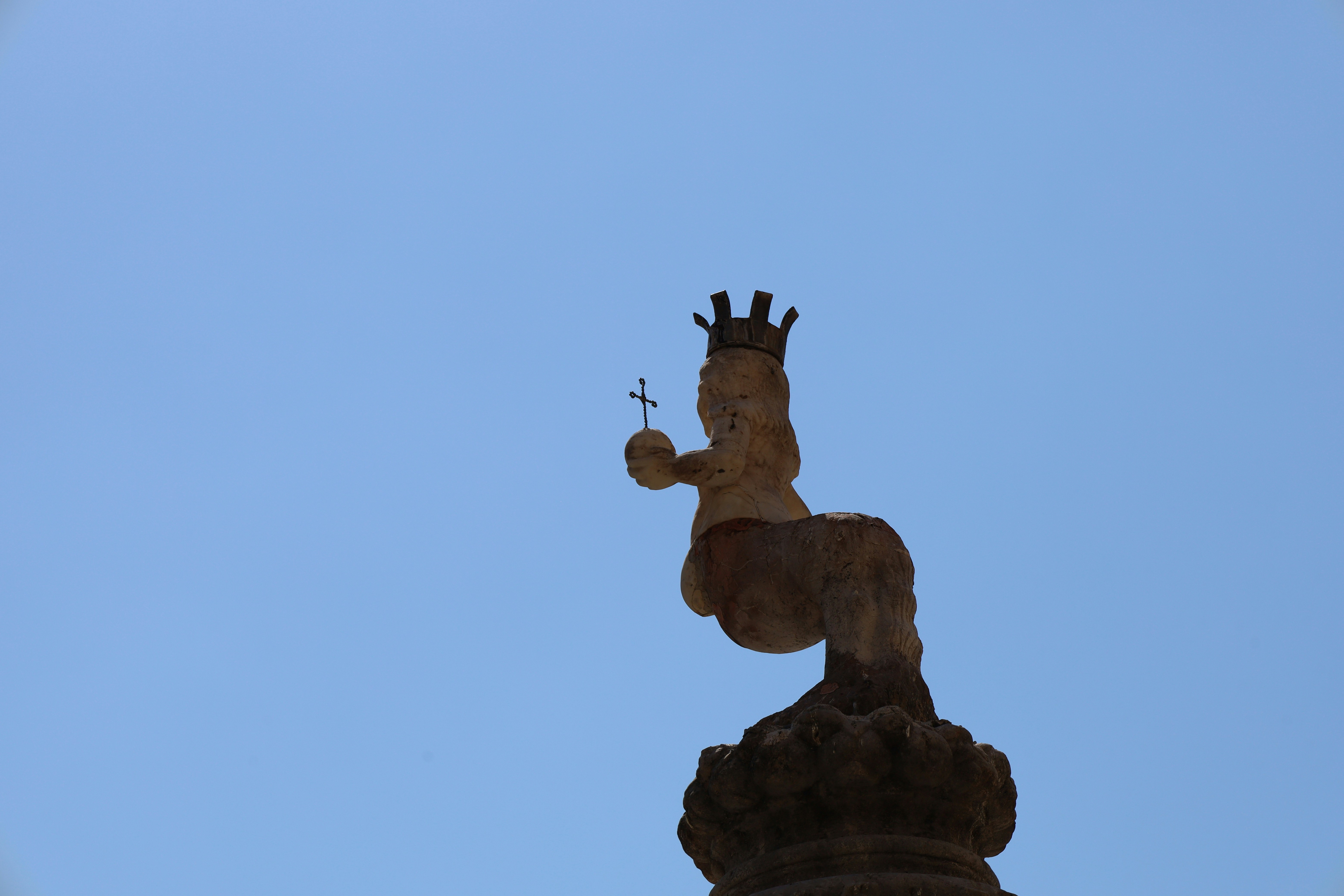 Crowned Stone Spire: A RomanesqueWeathervane Statuette Against Open Sky