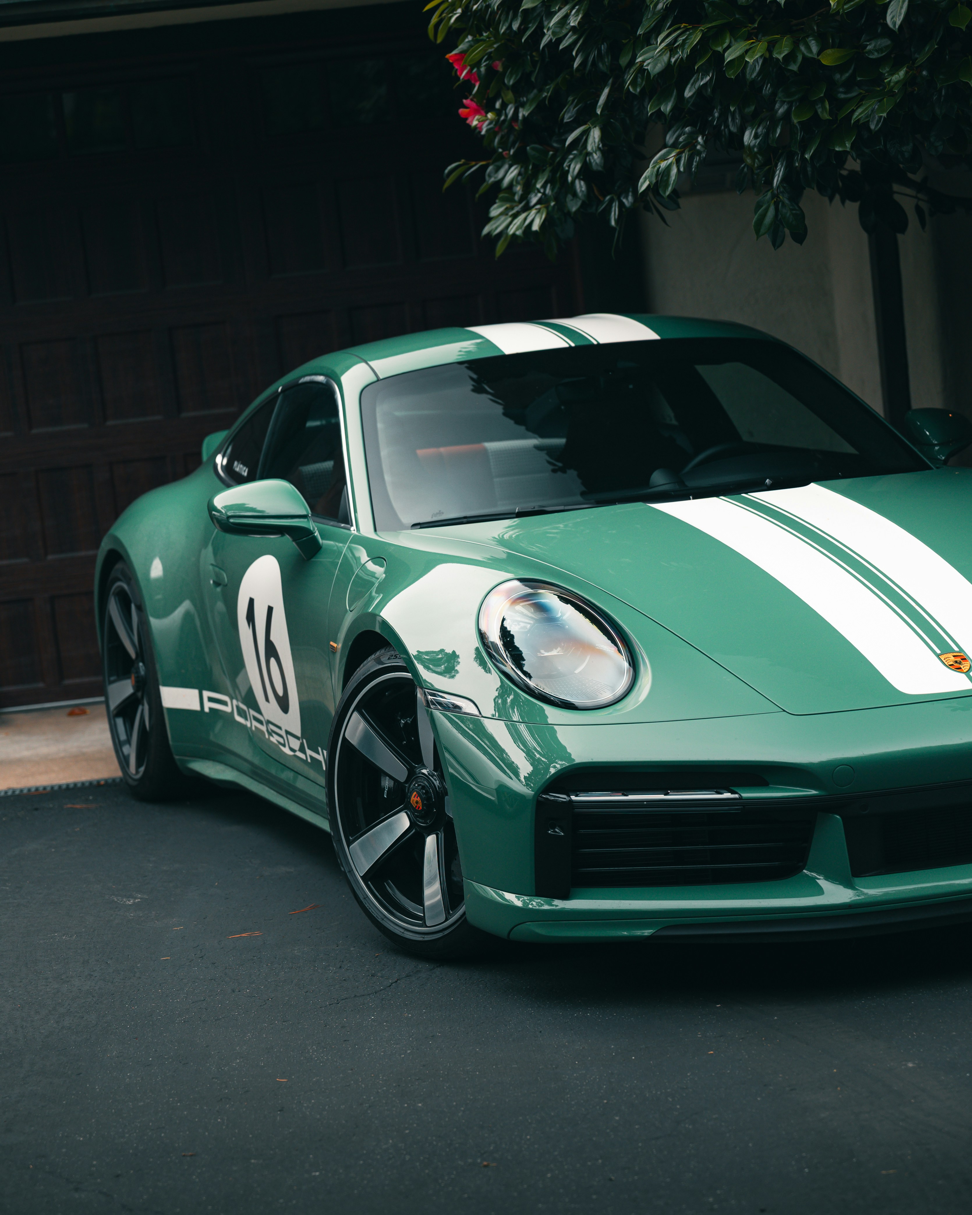 Green Porsche 911 with racing stripes tucked beside a garage