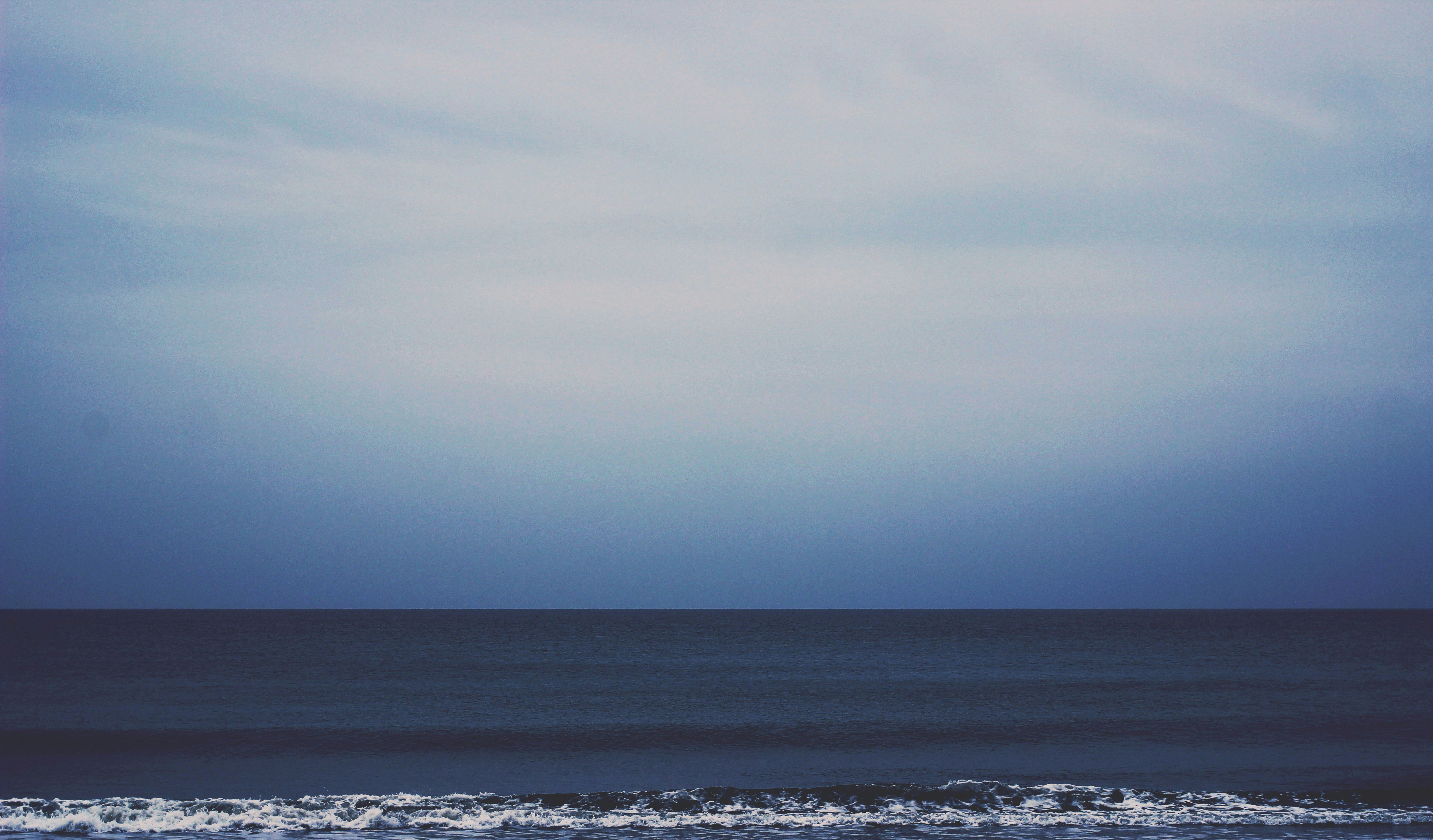 Long, calm horizon over a darkened sea with a gentle gradient sky; minimal elements, serene seascape with subtle waves near shore. It is a landscape photograph.