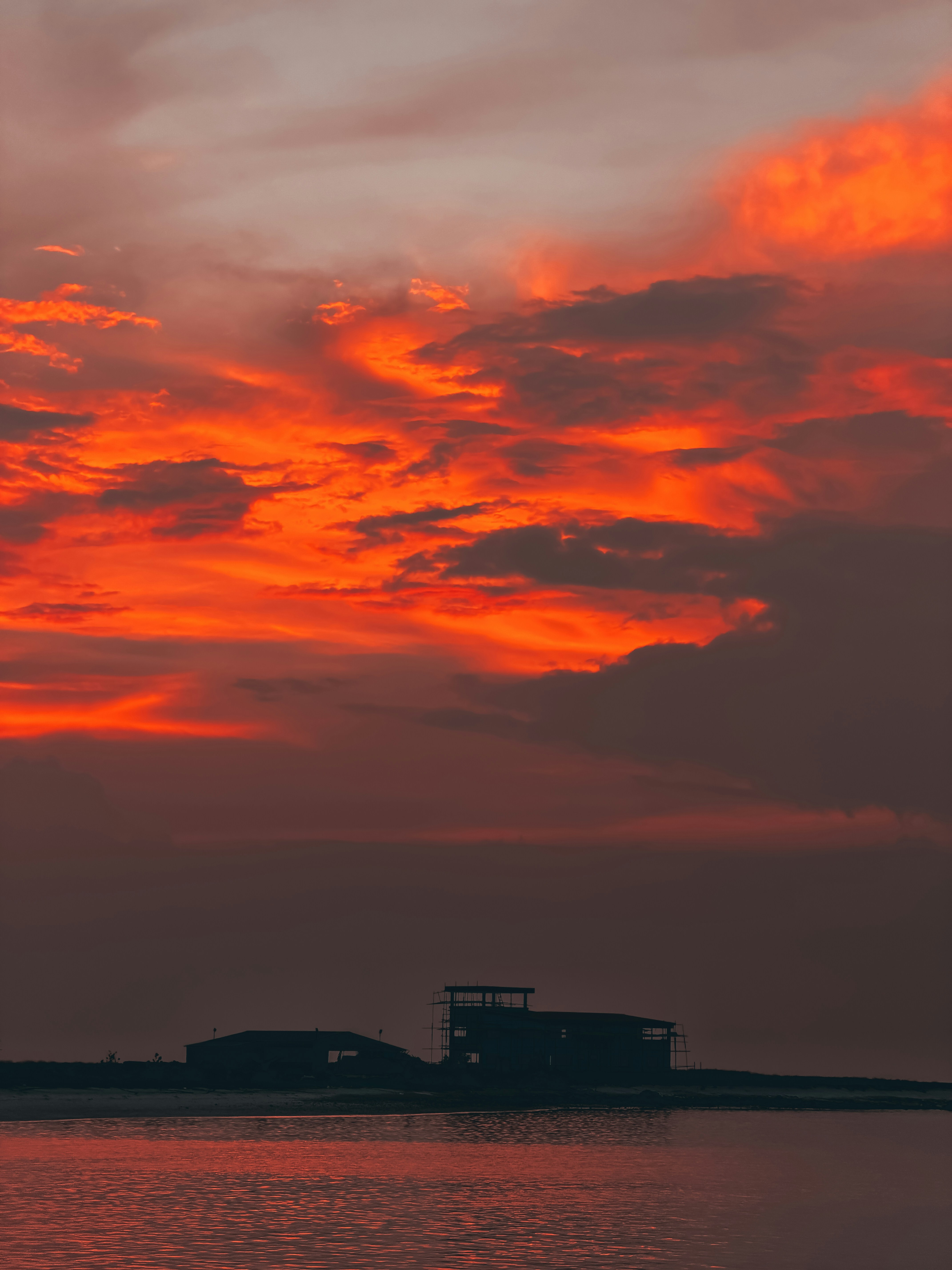 Dramatic orange clouds hover above a calm harbor with a low-contrast building silhouette on the horizon.