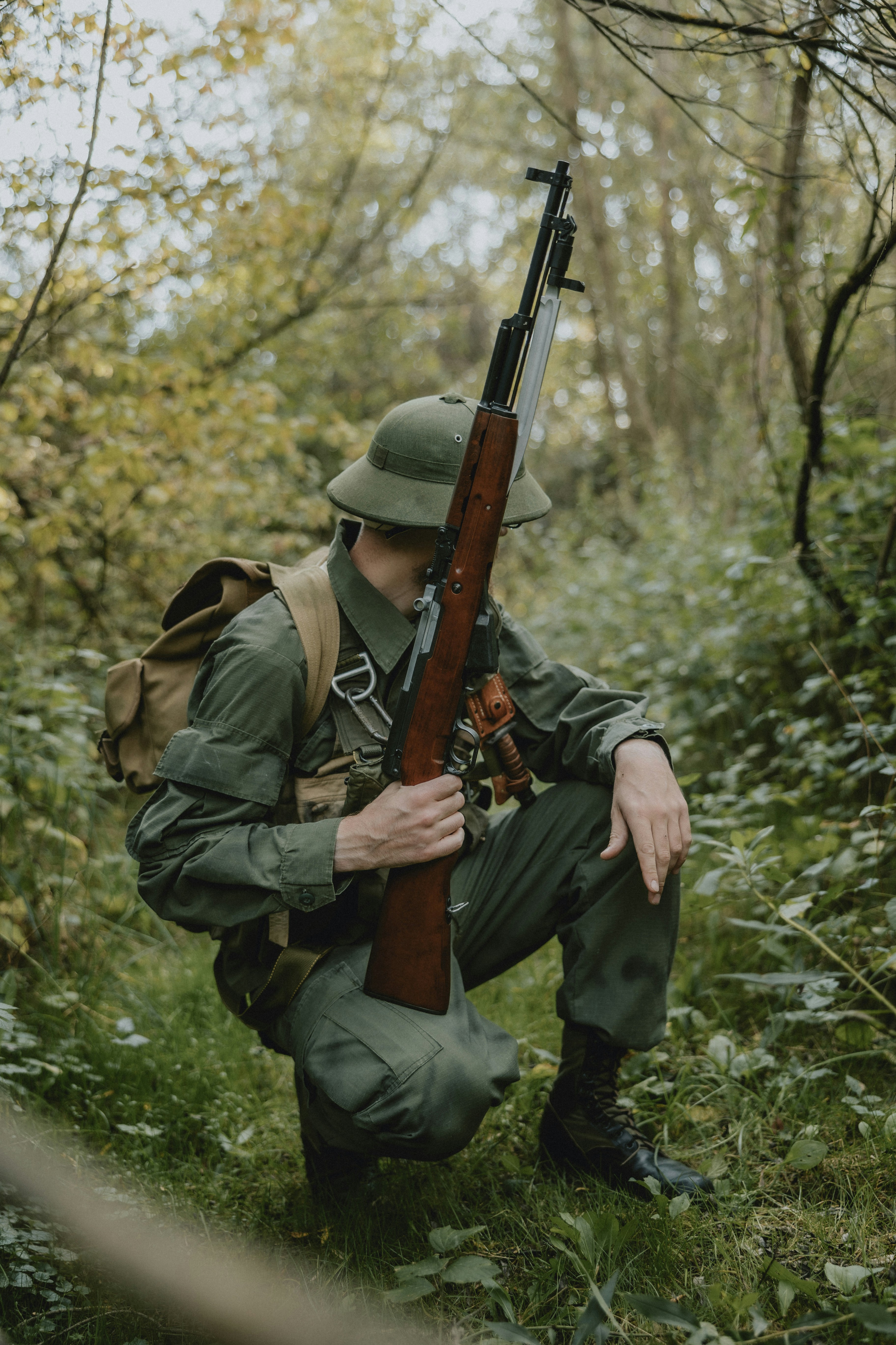 Green soldier in a forest crouch with rifle resting on shoulder
