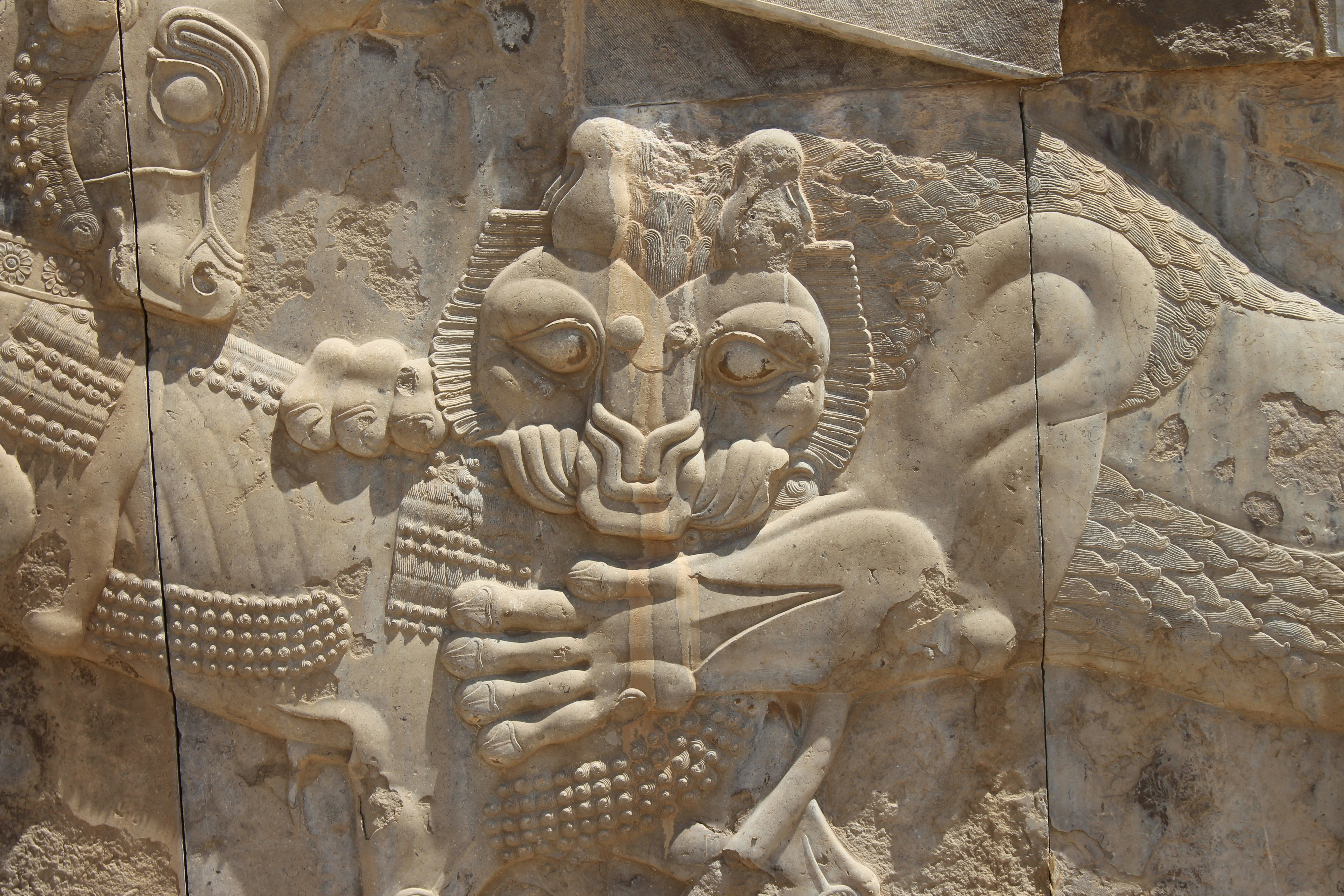 Carved stone relief featuring a masked figure with intertwined serpentine elements and ornate patterns, highlighting ancient artistry and weathered texture.
