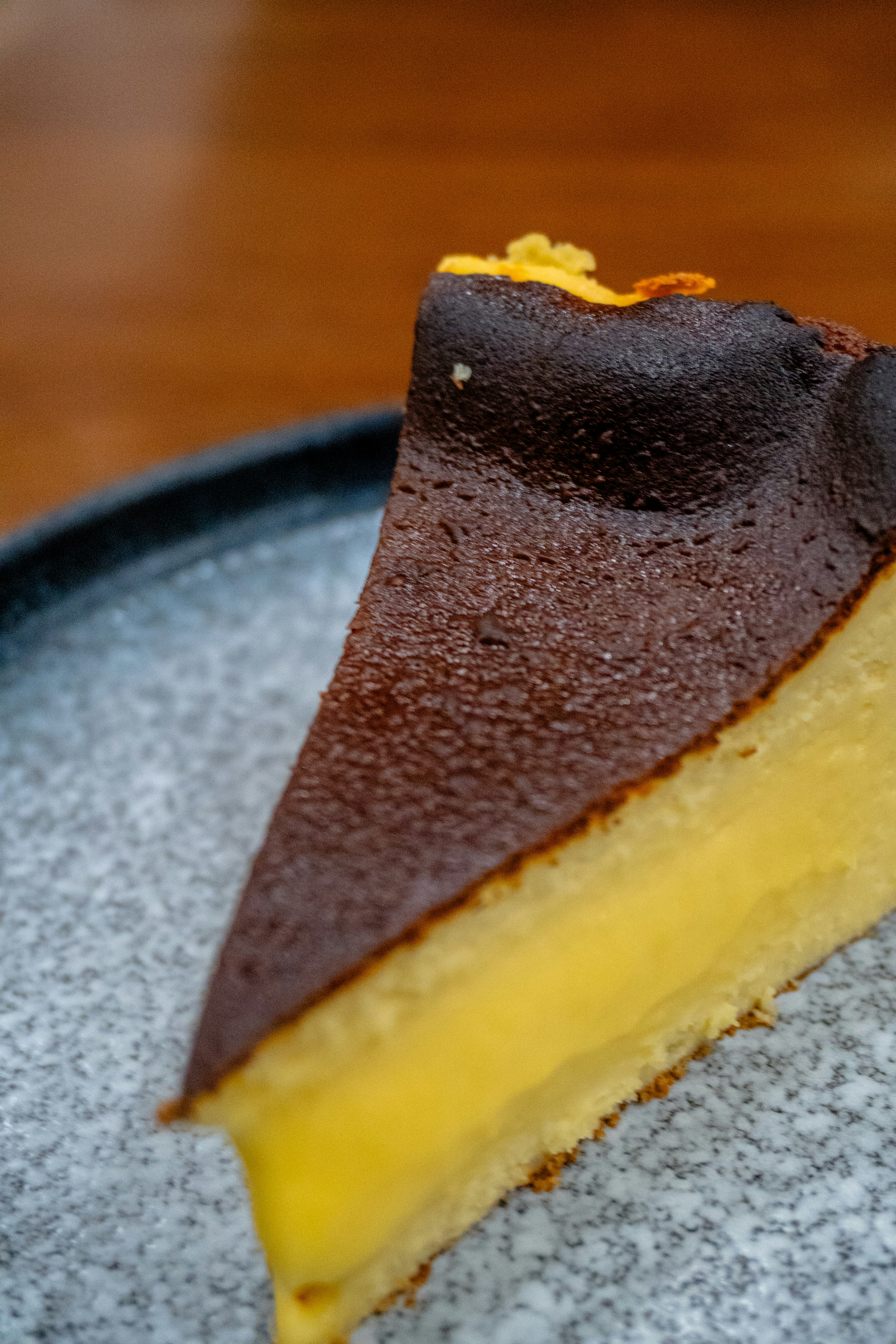 A slice of chocolate-topped custard pie rests on a textured plate, showcasing a contrast between dark cocoa crust and pale yellow filling.