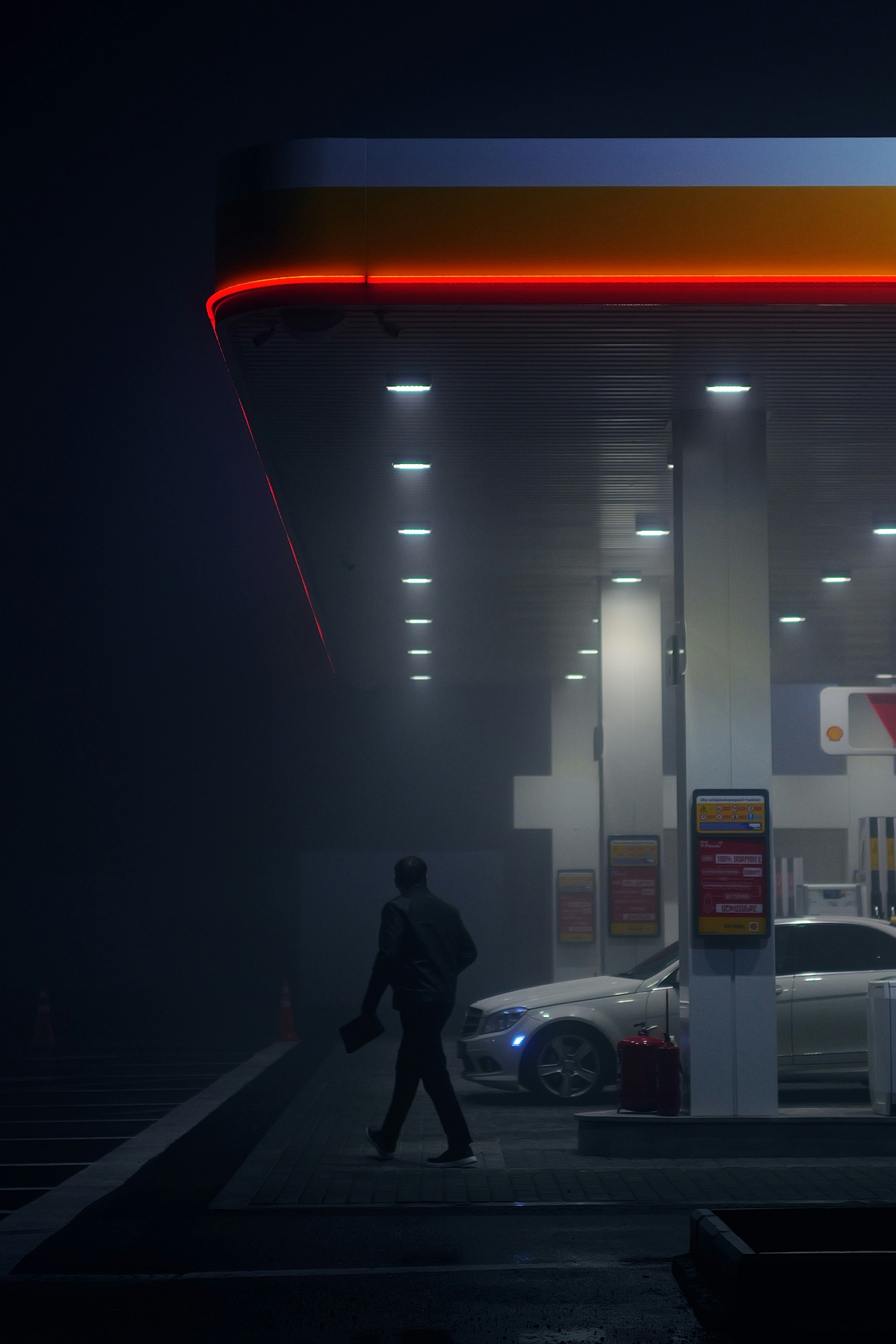 A solitary figure walks past a dimly lit gas station at night, softened by blue haze and neon accents.