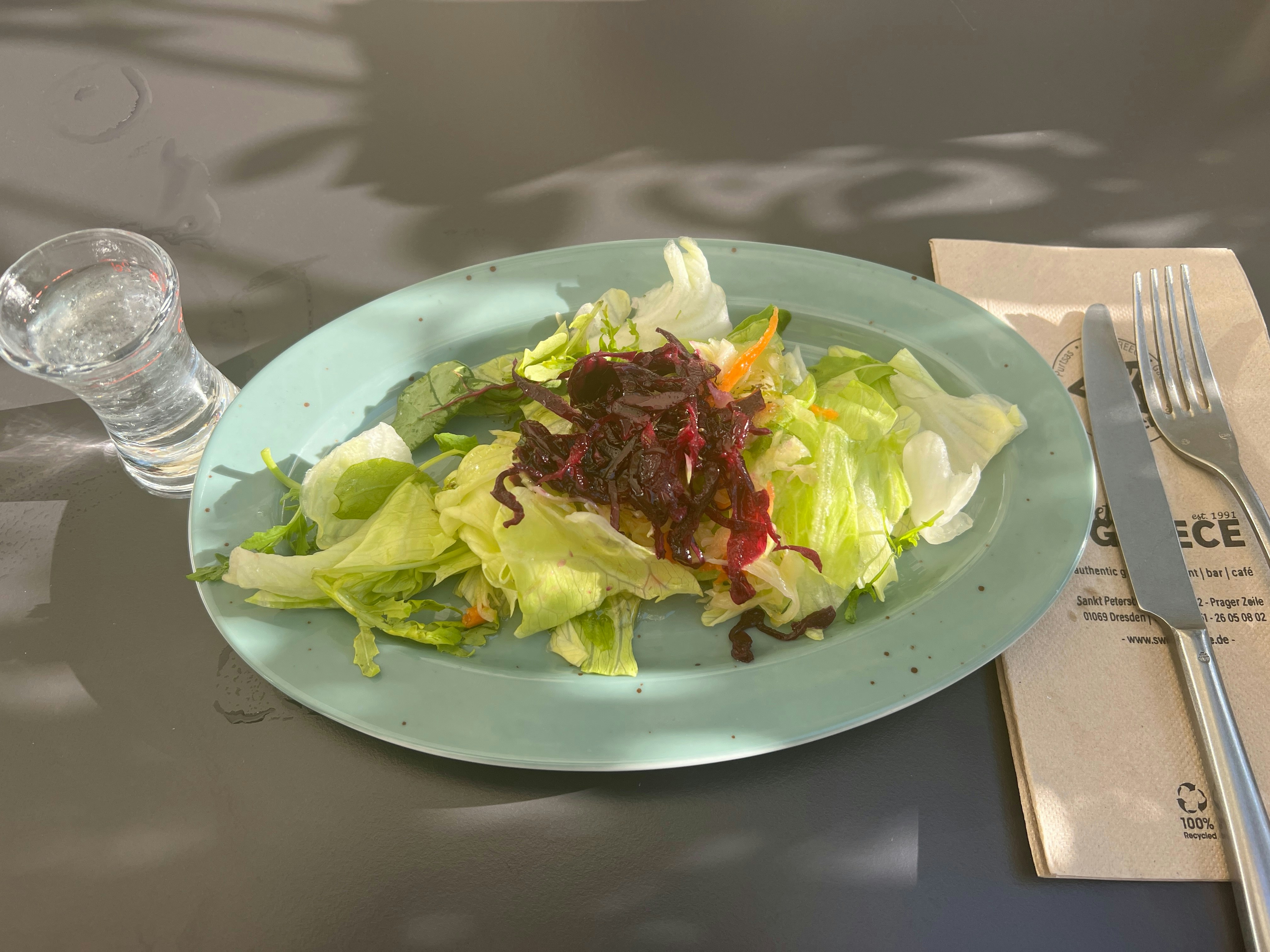 Green salad on a pale blue plate beside cutlery and a glass of water
