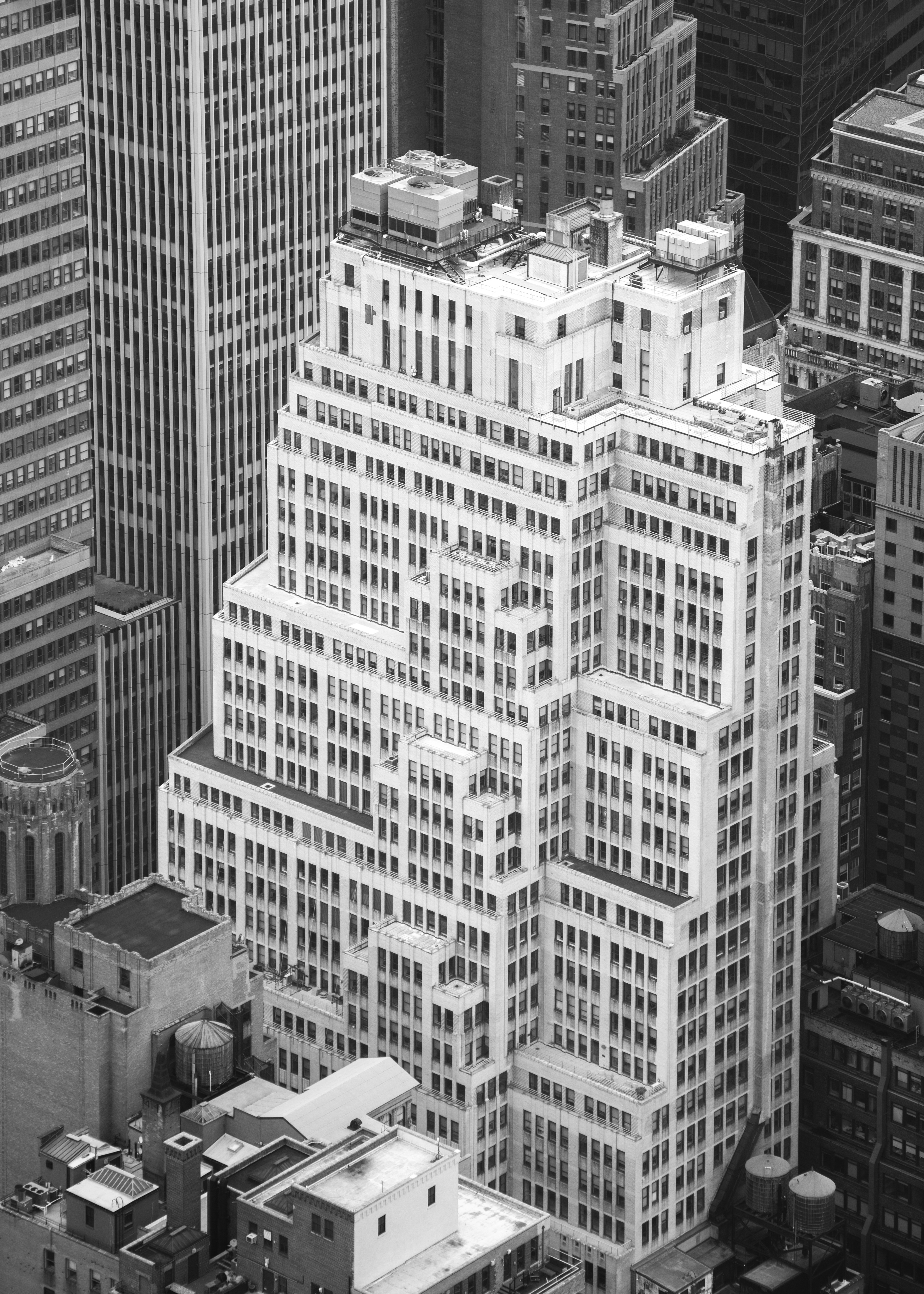 Monochrome tower with stepped, geometric details rises among surrounding skyscrapers, emphasizing texture and rhythm of early-20th-century architecture.