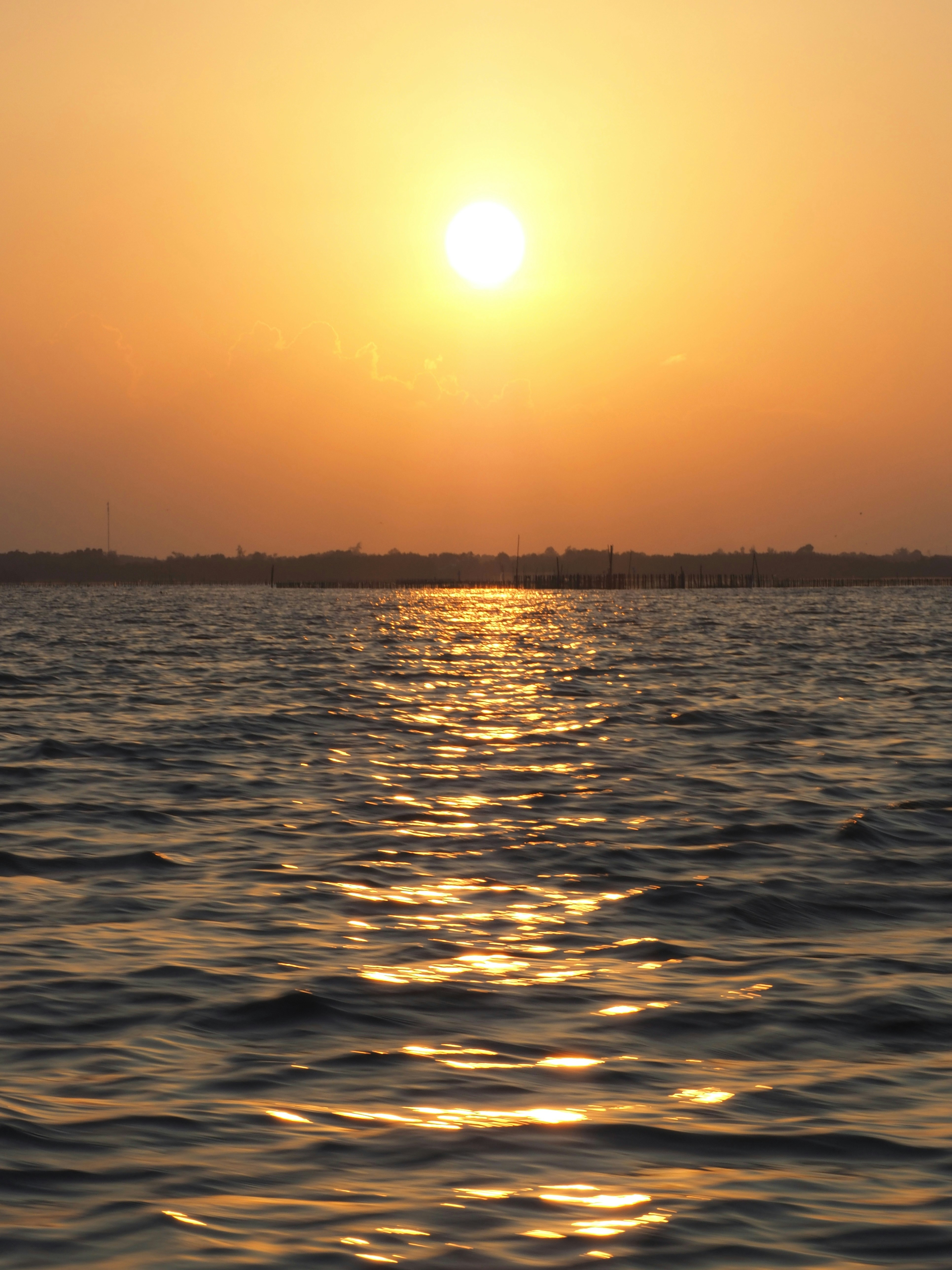 Warm sunset over calm waves reflecting golden light; distant shoreline silhouettes and a serene water surface.