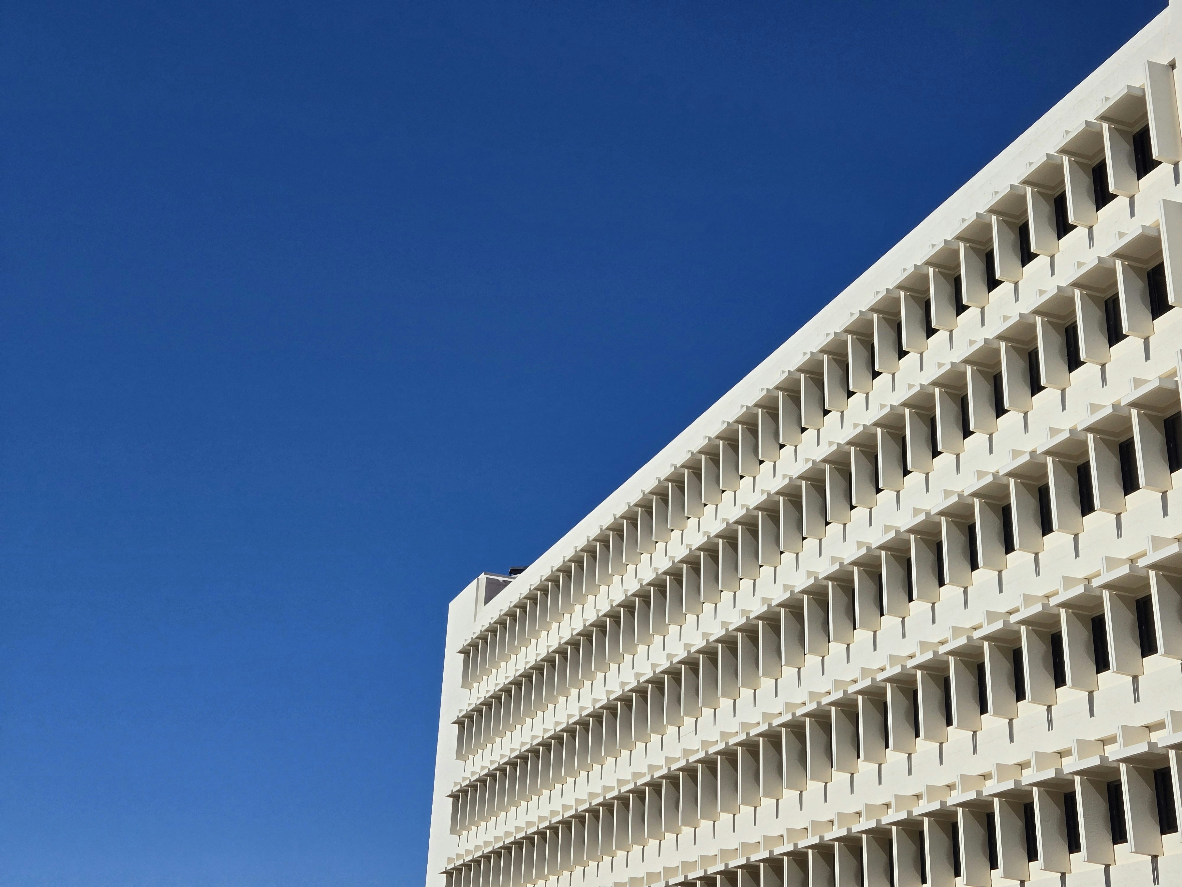 Architectural facade with repetitive rectangular openings under a clear blue sky, captured at a wide urban angle to emphasize depth and structure.