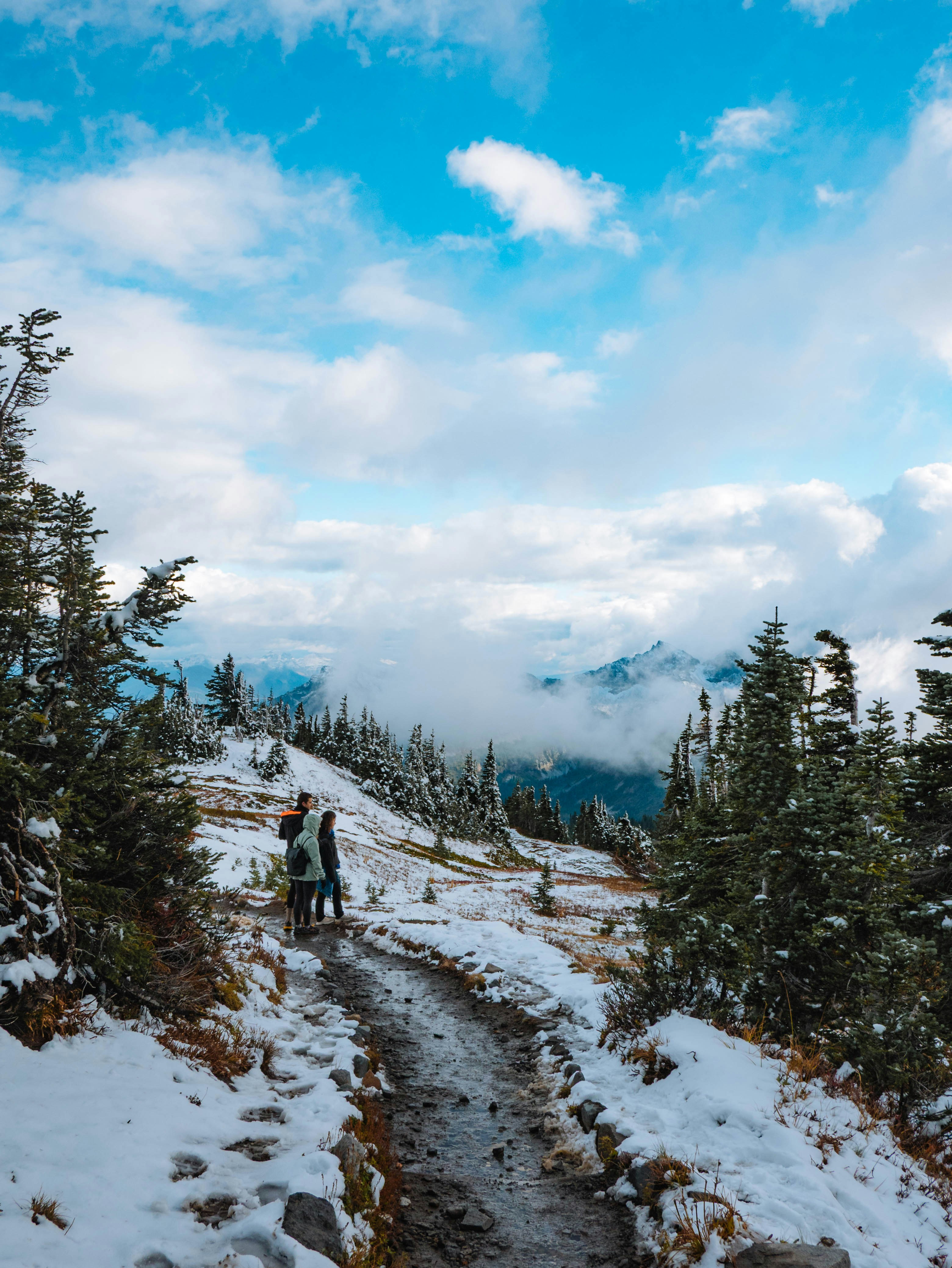 Snowbound Summit: Two hikers on a winding path under a blue, cloud-dotted sky